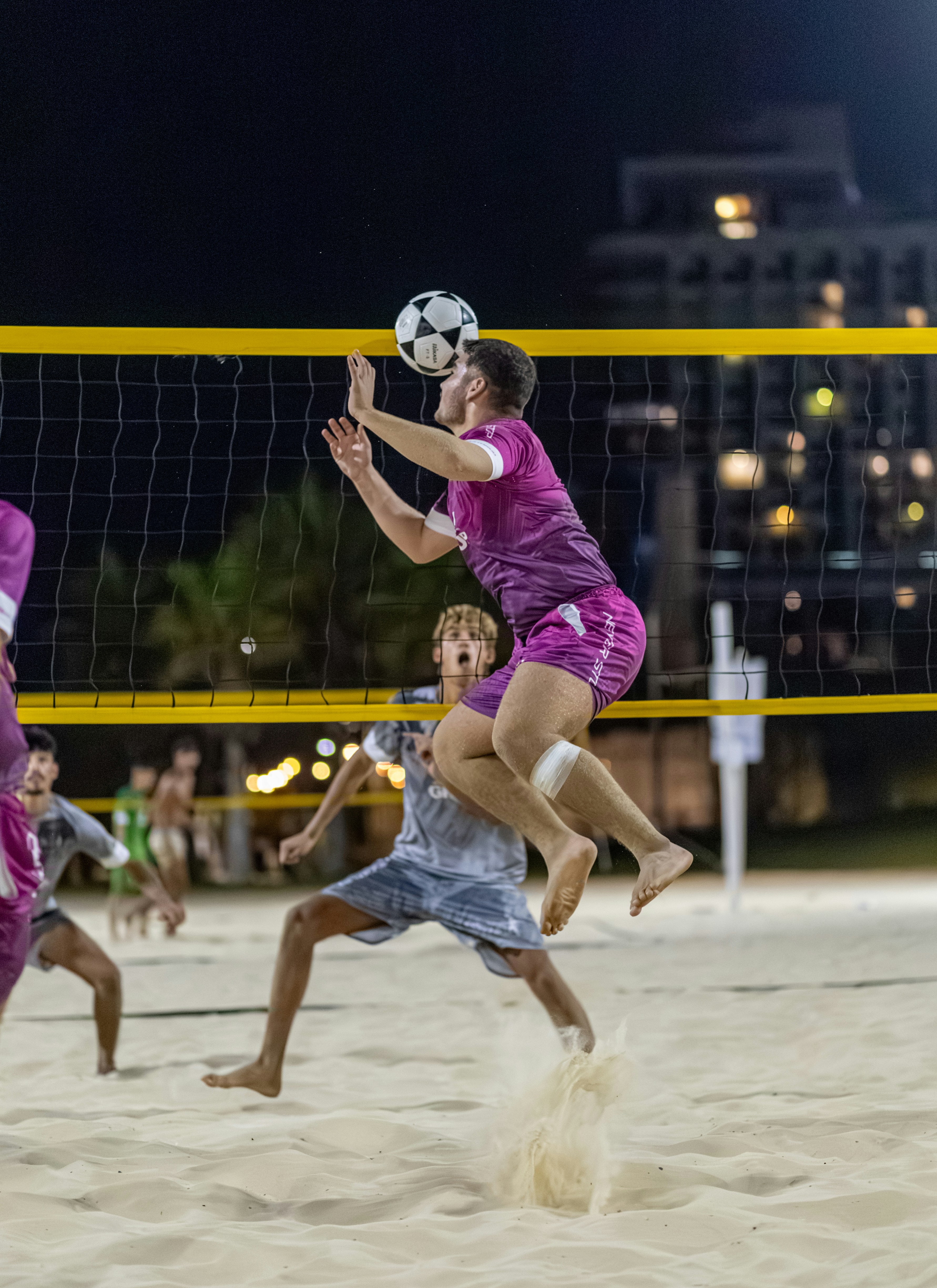 Mid-air volley under arena lights: a purple-clad attacker soars toward the ball