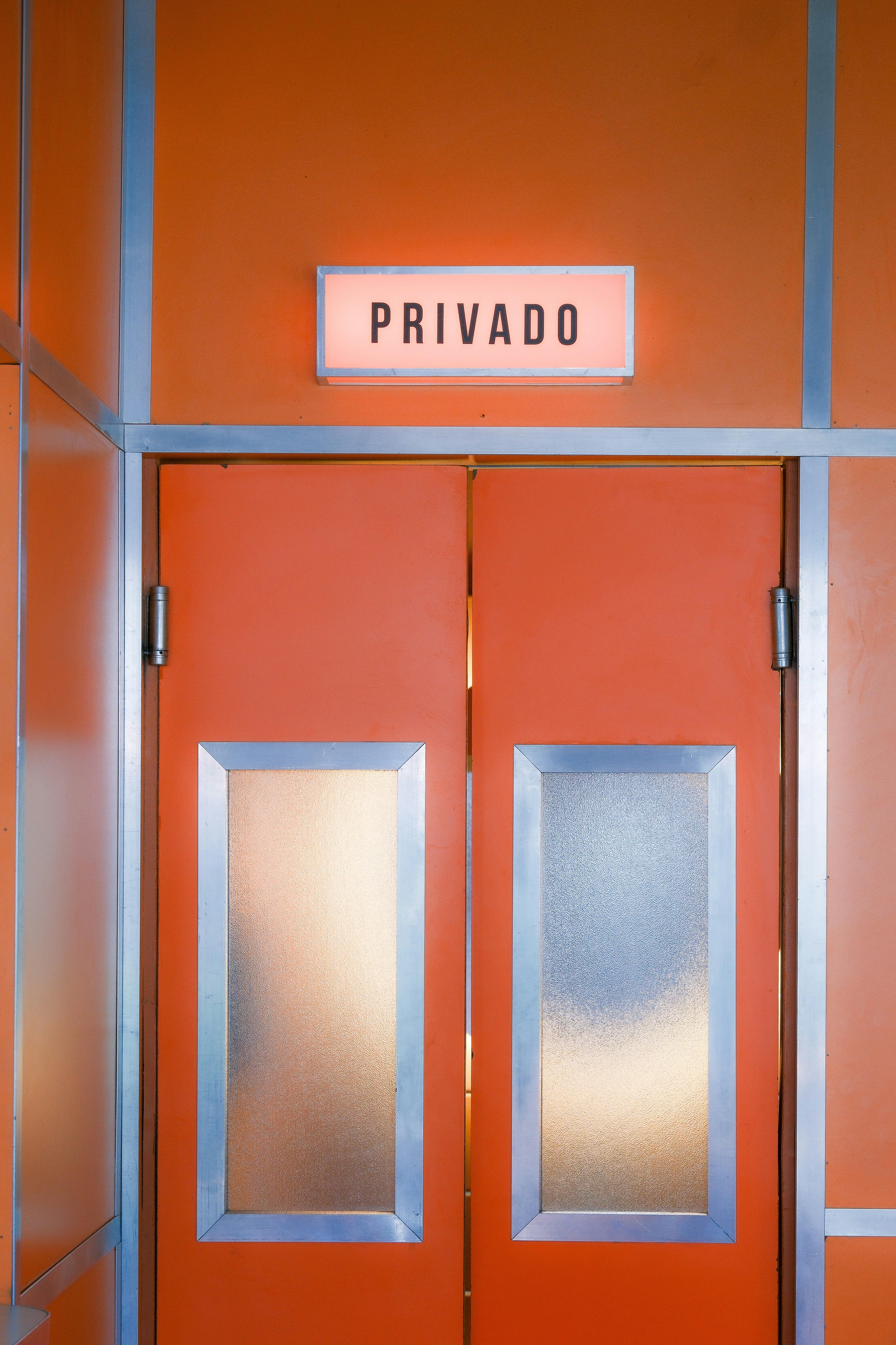 A striking orange “Privado” door framed with metallic details, blending retro design and bold color.