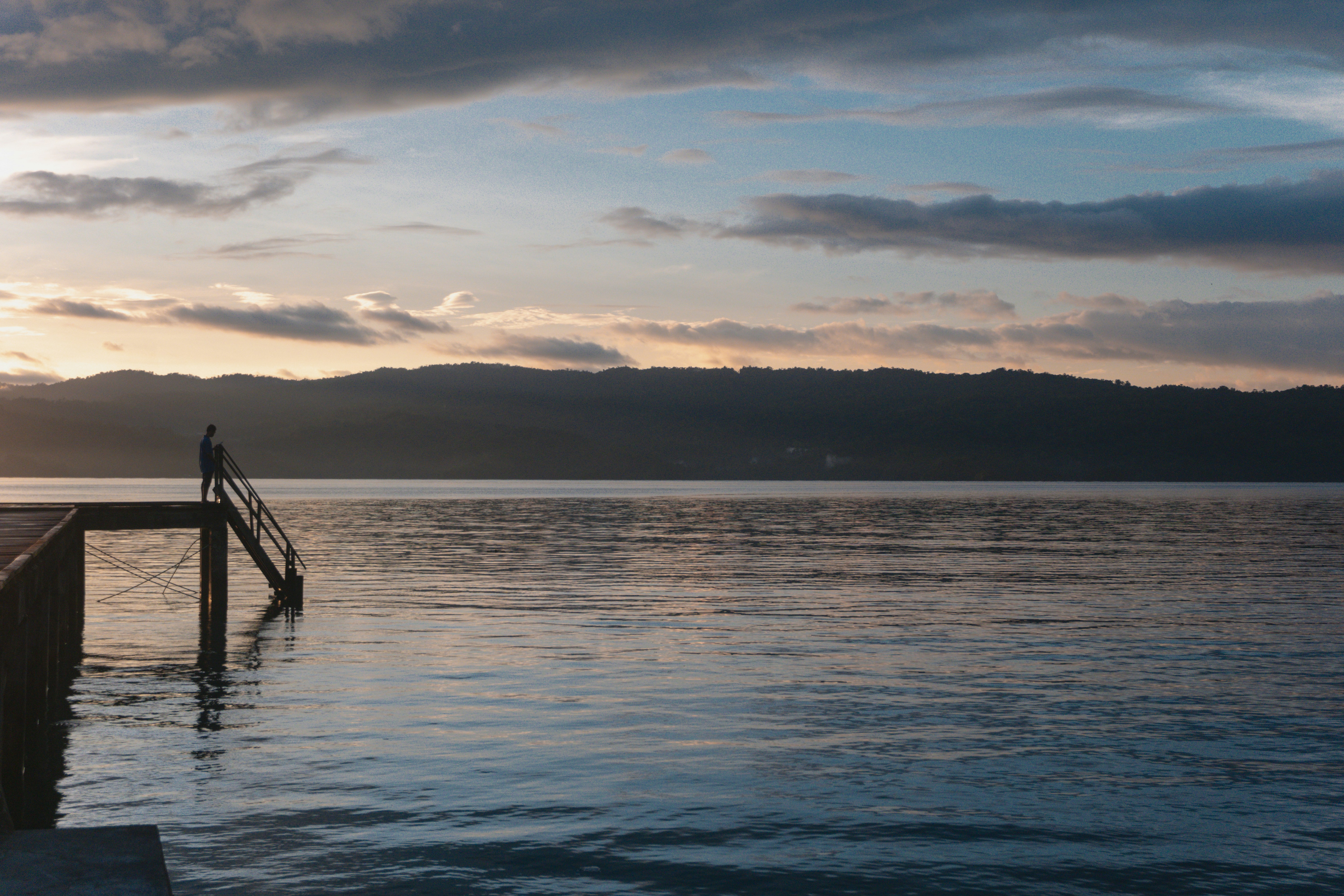 Lone Figure at the Pier as Sunset Reflects on a Quiet Lake