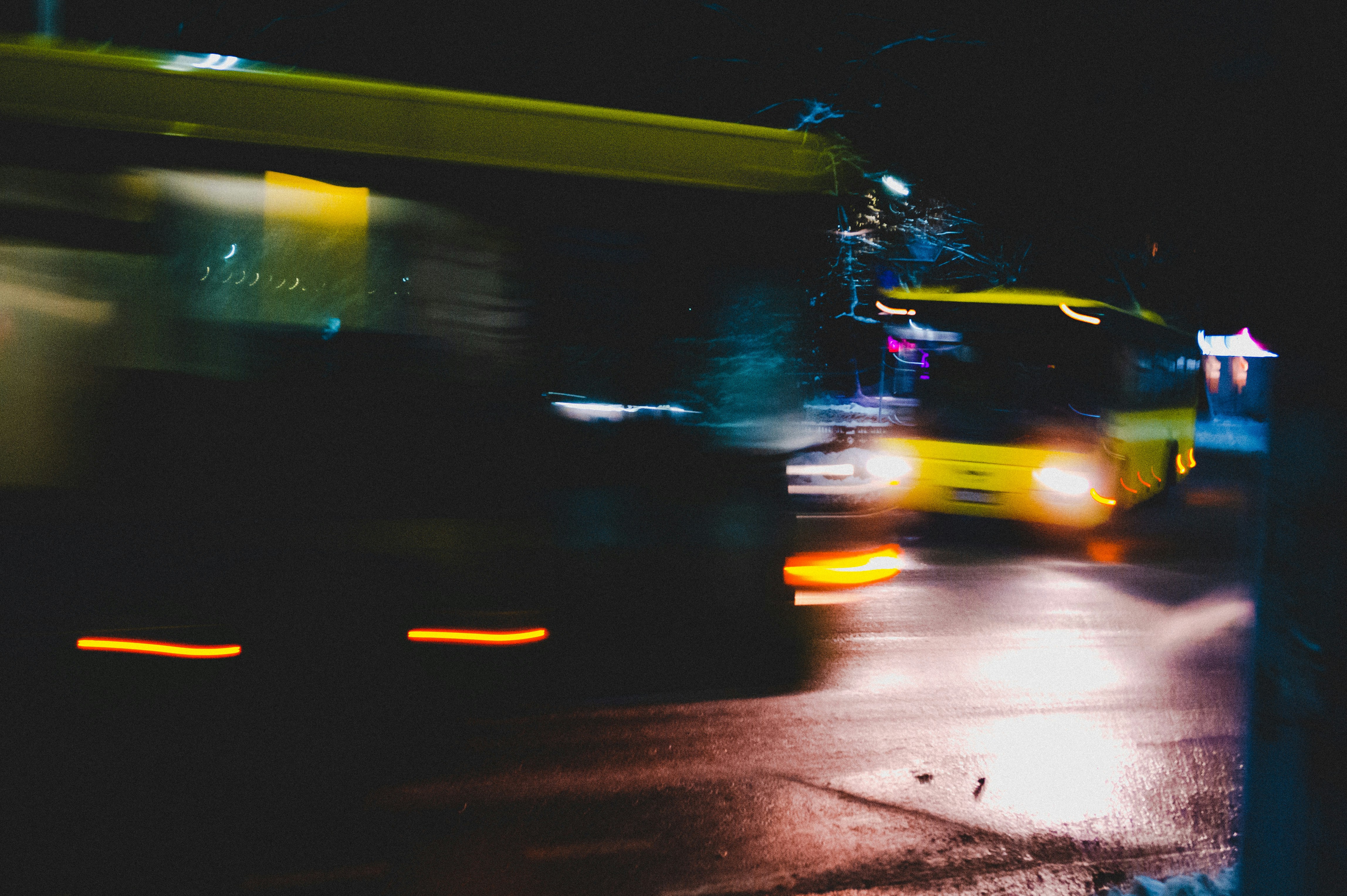 A yellow bus streaks through the night, captured with motion blur that emphasizes the speed and vibrant lights of the urban scene.