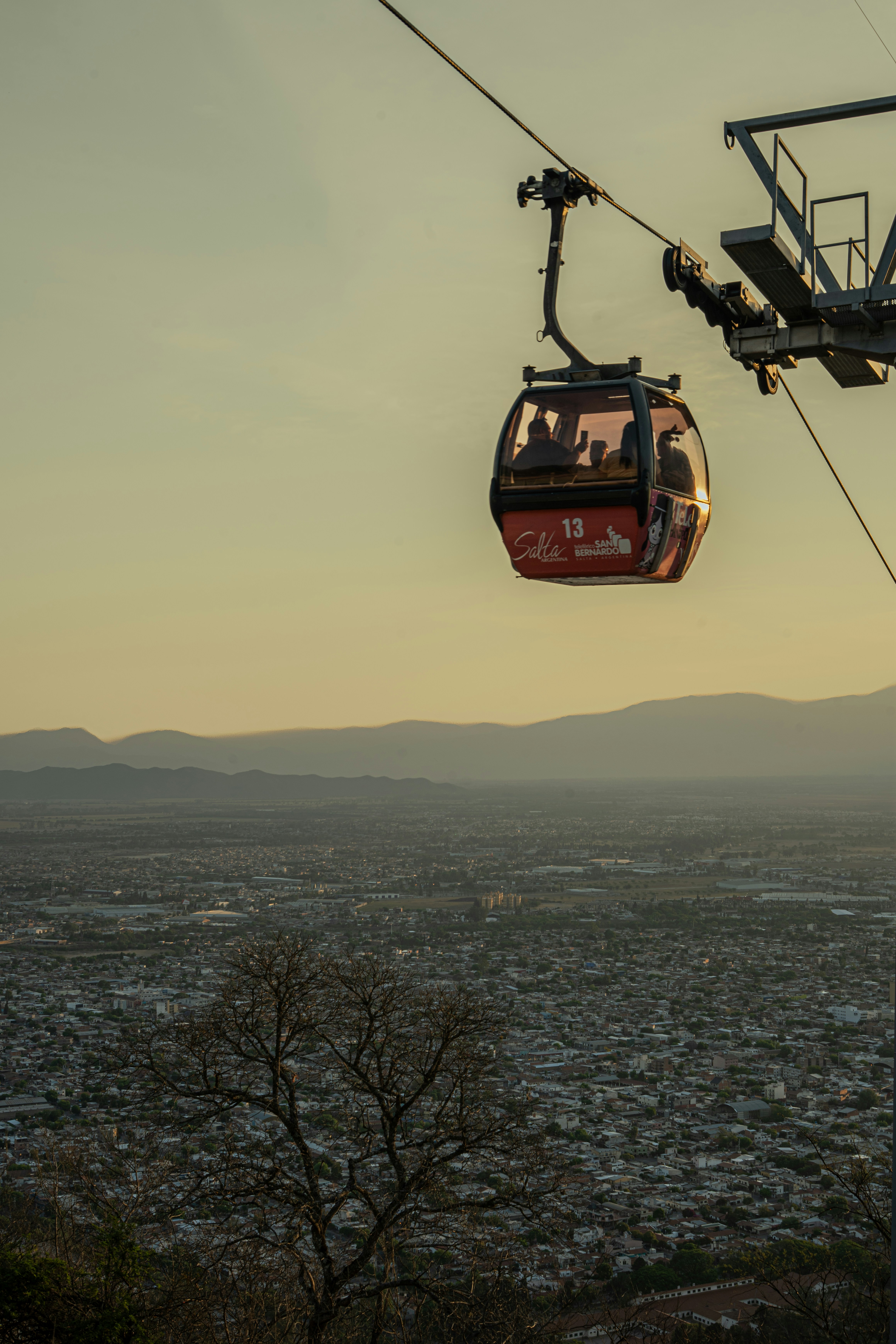 Red gondola glides above a sunlit city at dusk