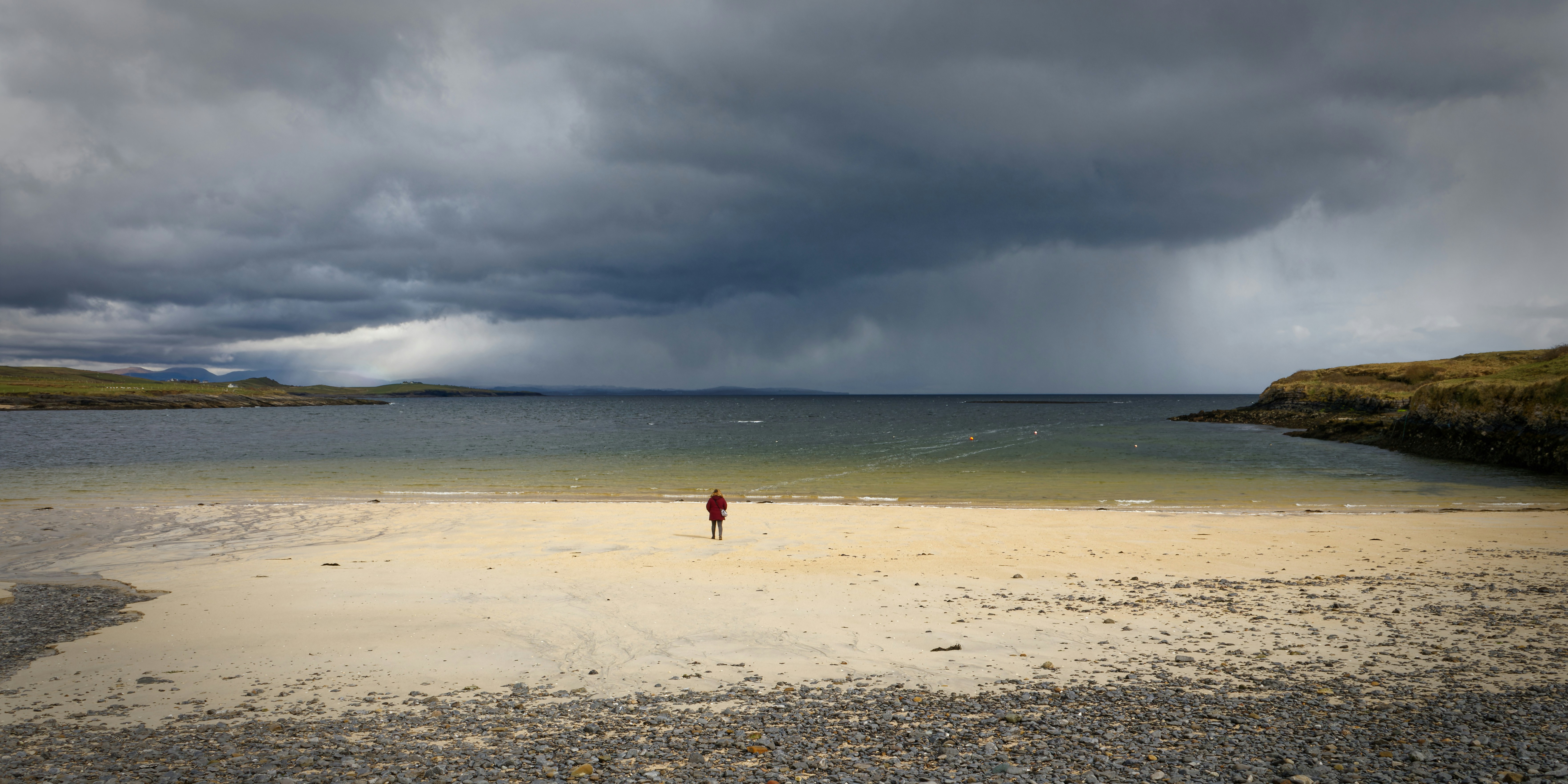 Lone Figure on a Quiet Beach as Storm Clouds Gather