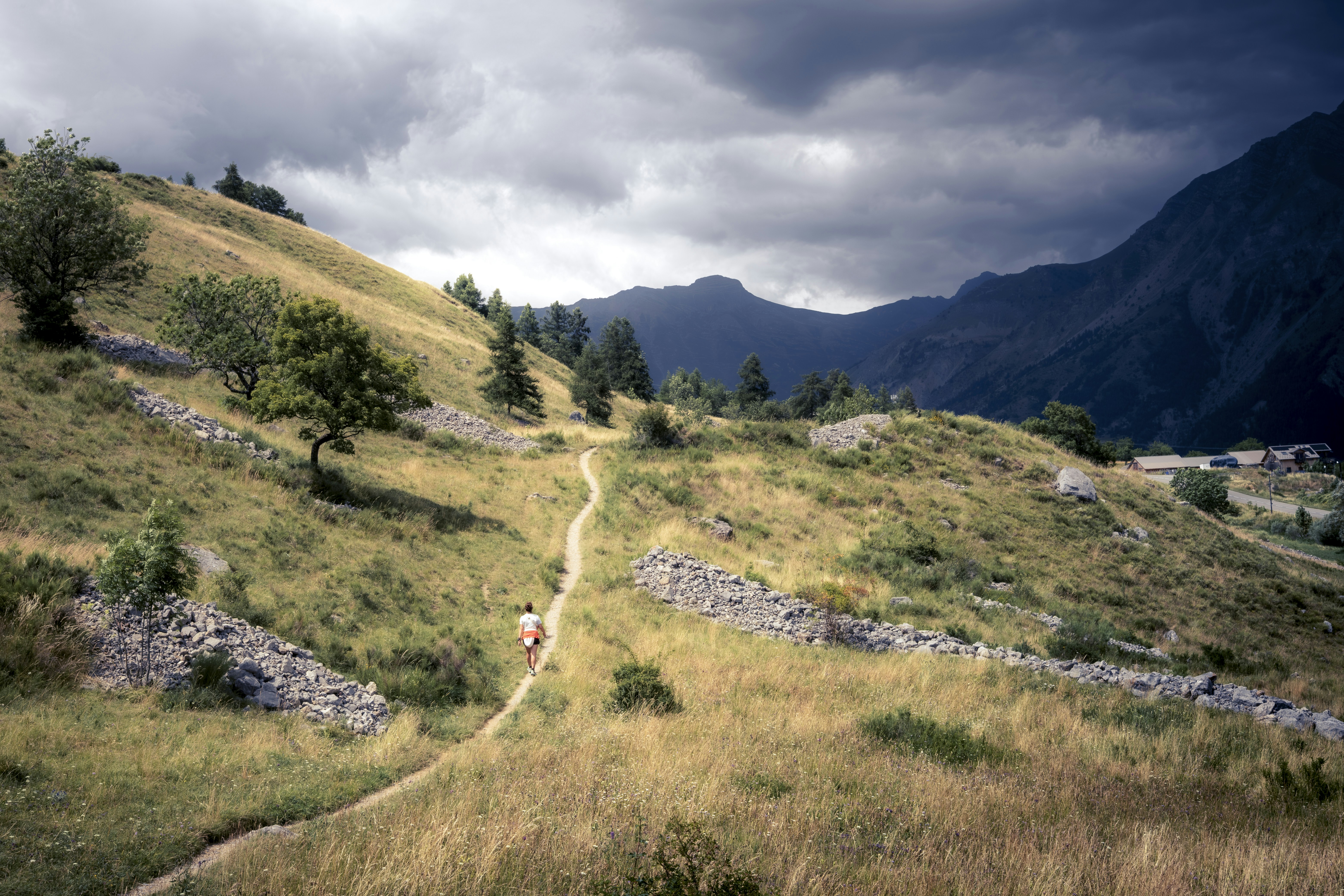 A lone hiker threads a grassy ridge toward distant peaks