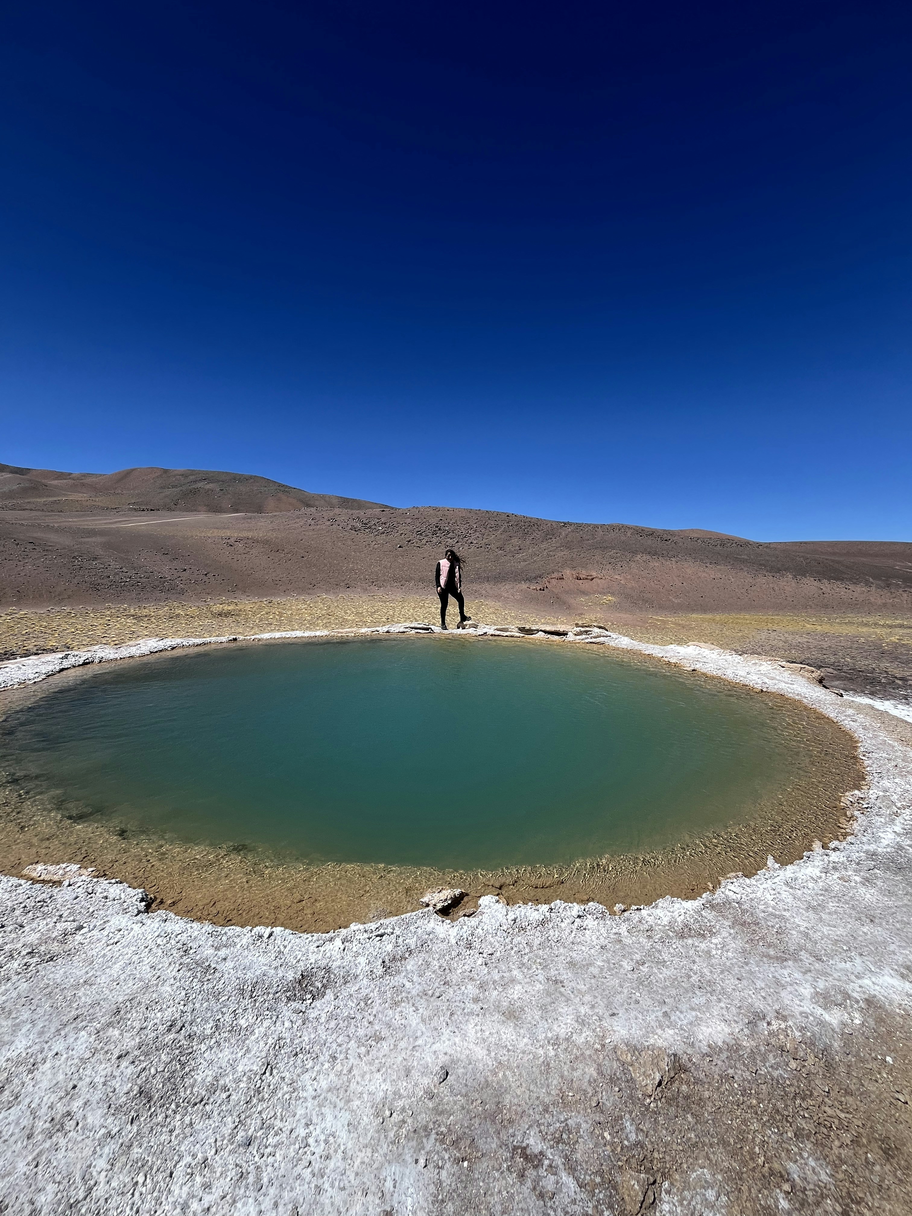  solitary figure on a mineral pool rim beneath a vast blue sky