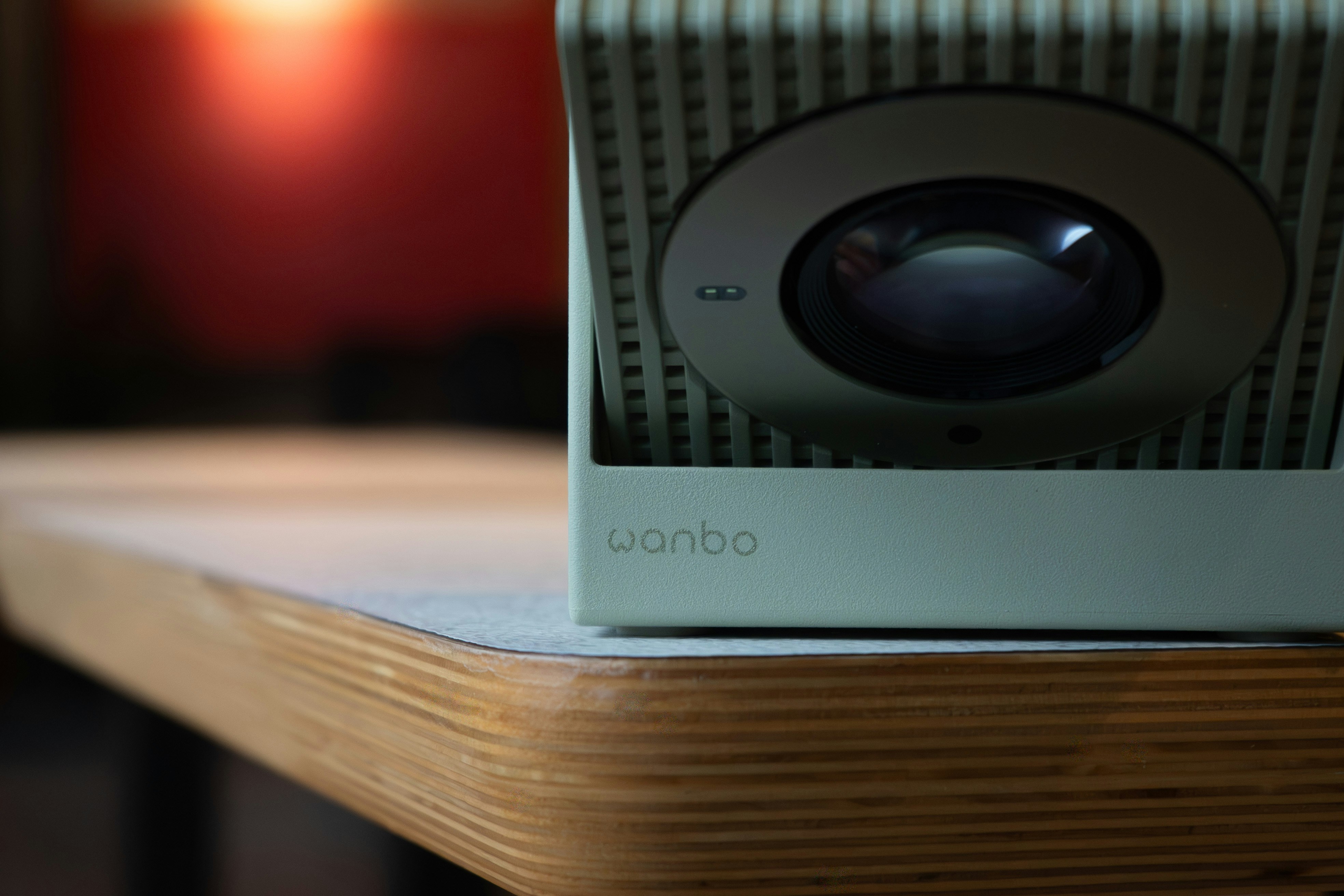 A minimalist portable projector sits on a wooden table. Soft ambient lighting creates a cozy, home-cinema atmosphere, highlighting the projector’s modern design and texture. Perfect for tech, gadget, lifestyle, or productivity themes.