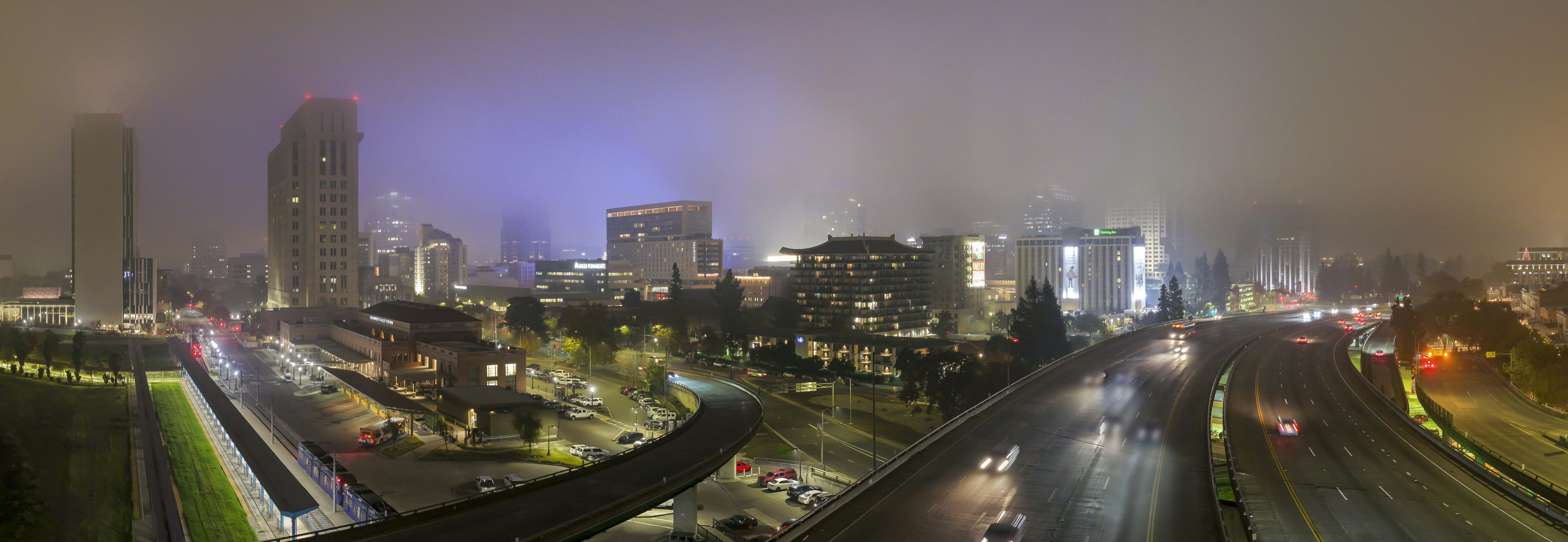 Cityscape at night with fog and illuminated buildings.