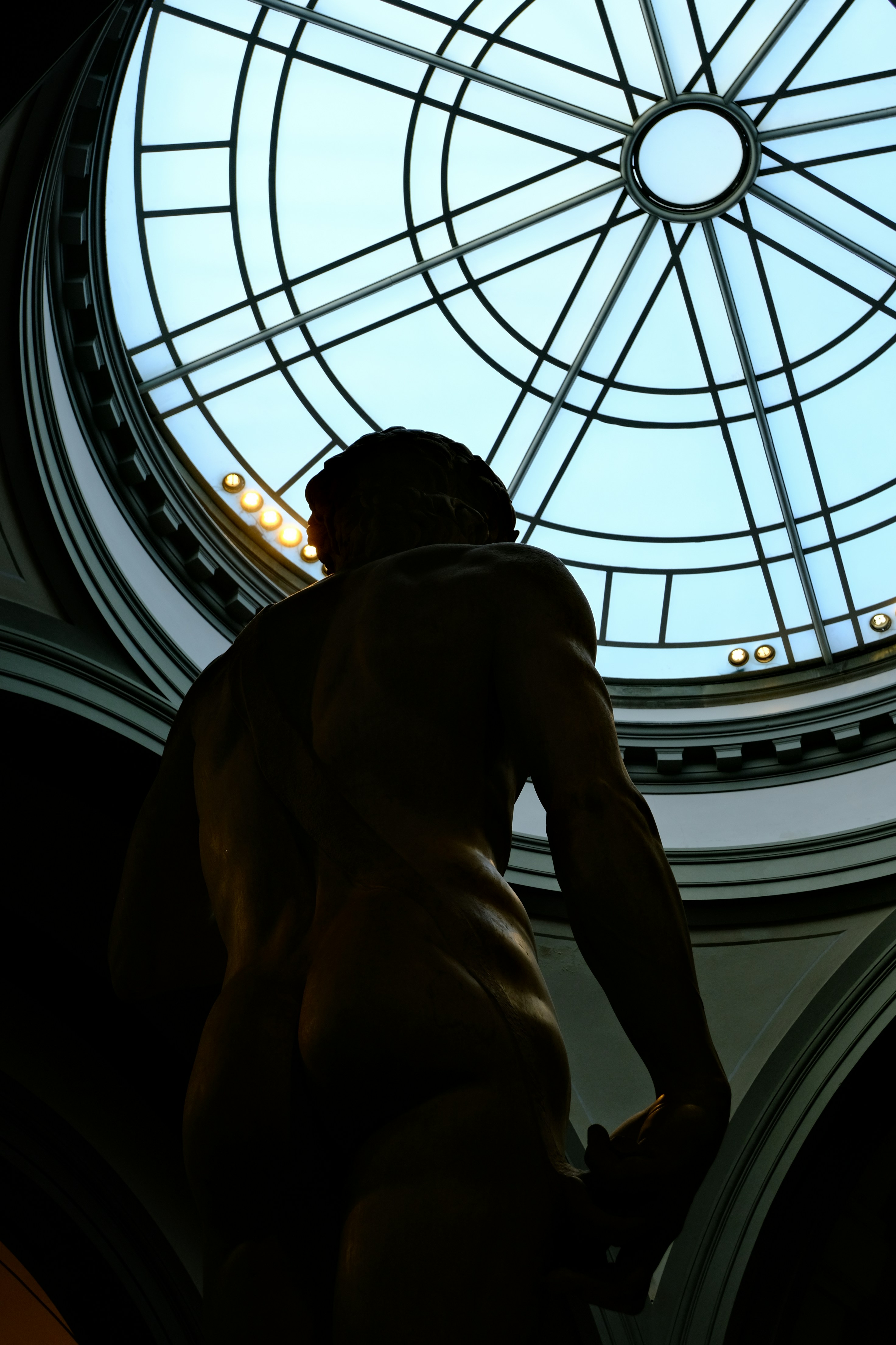 Statue Against Glass Sky: A Silhouette Under Clock-Wheel Architecture