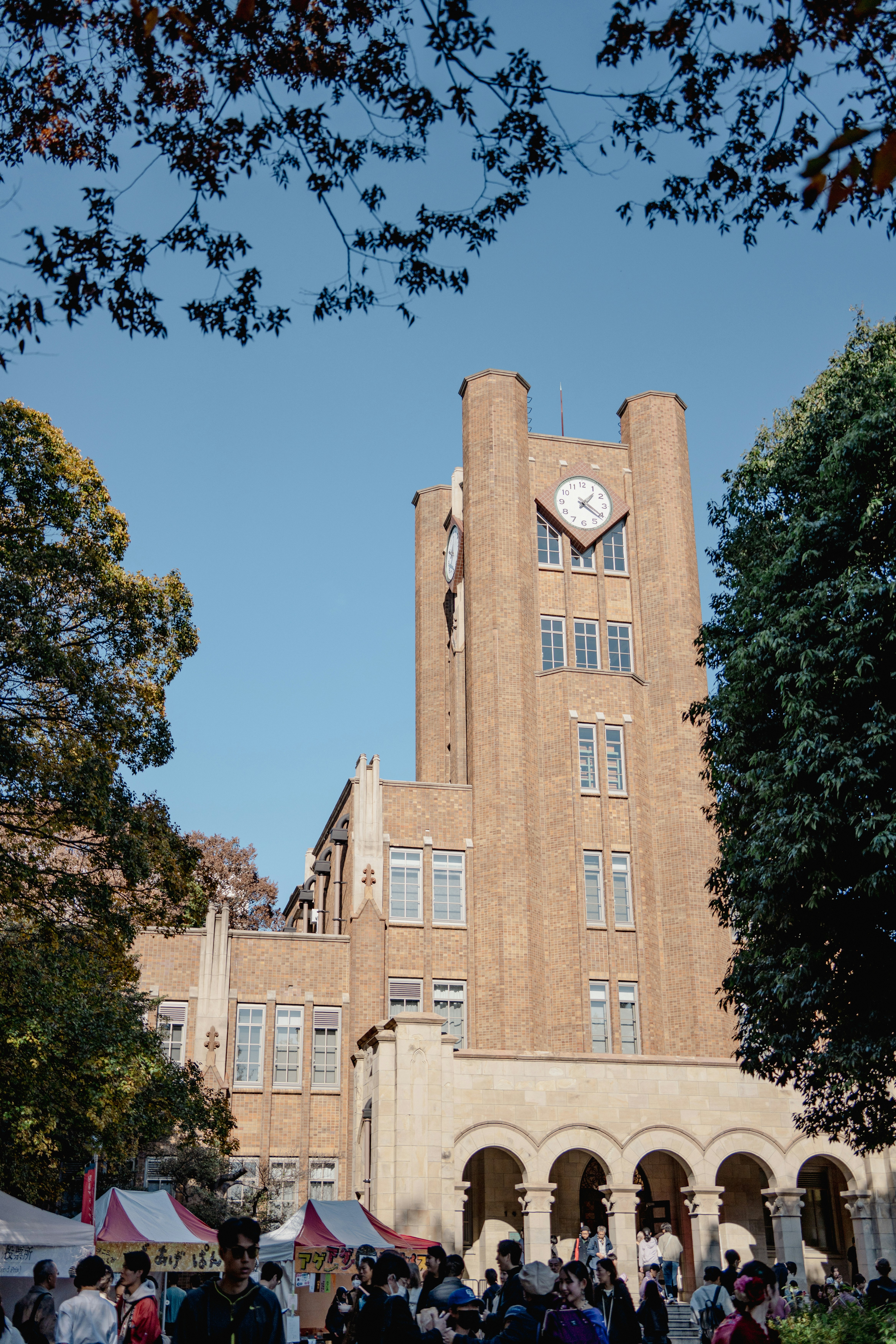 Clock-towered Campus Facade Framed by Tree Canopies During Market Day