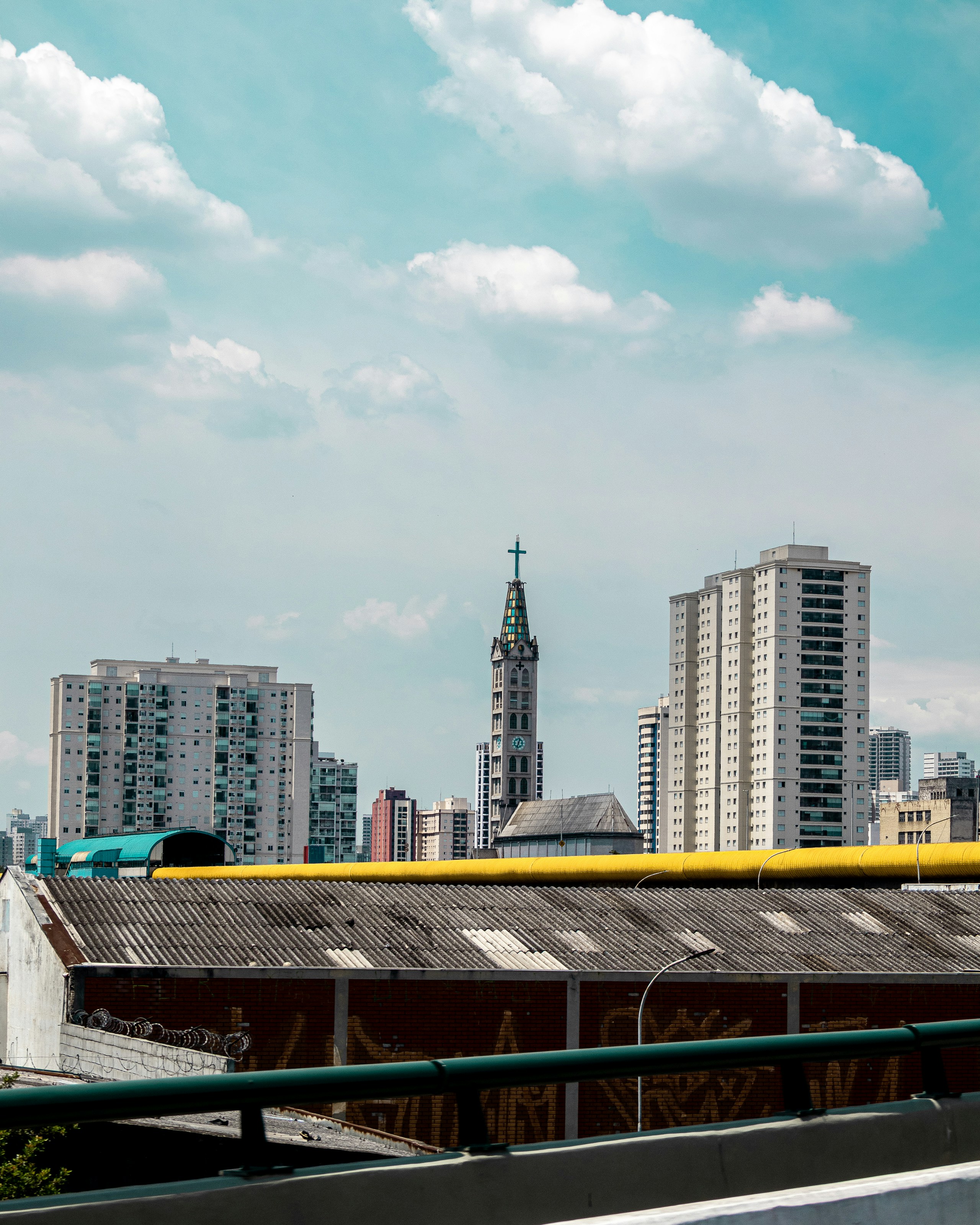 Spire reaching skyward, city sprawl below, industrial foreground, tranquil clouds above.