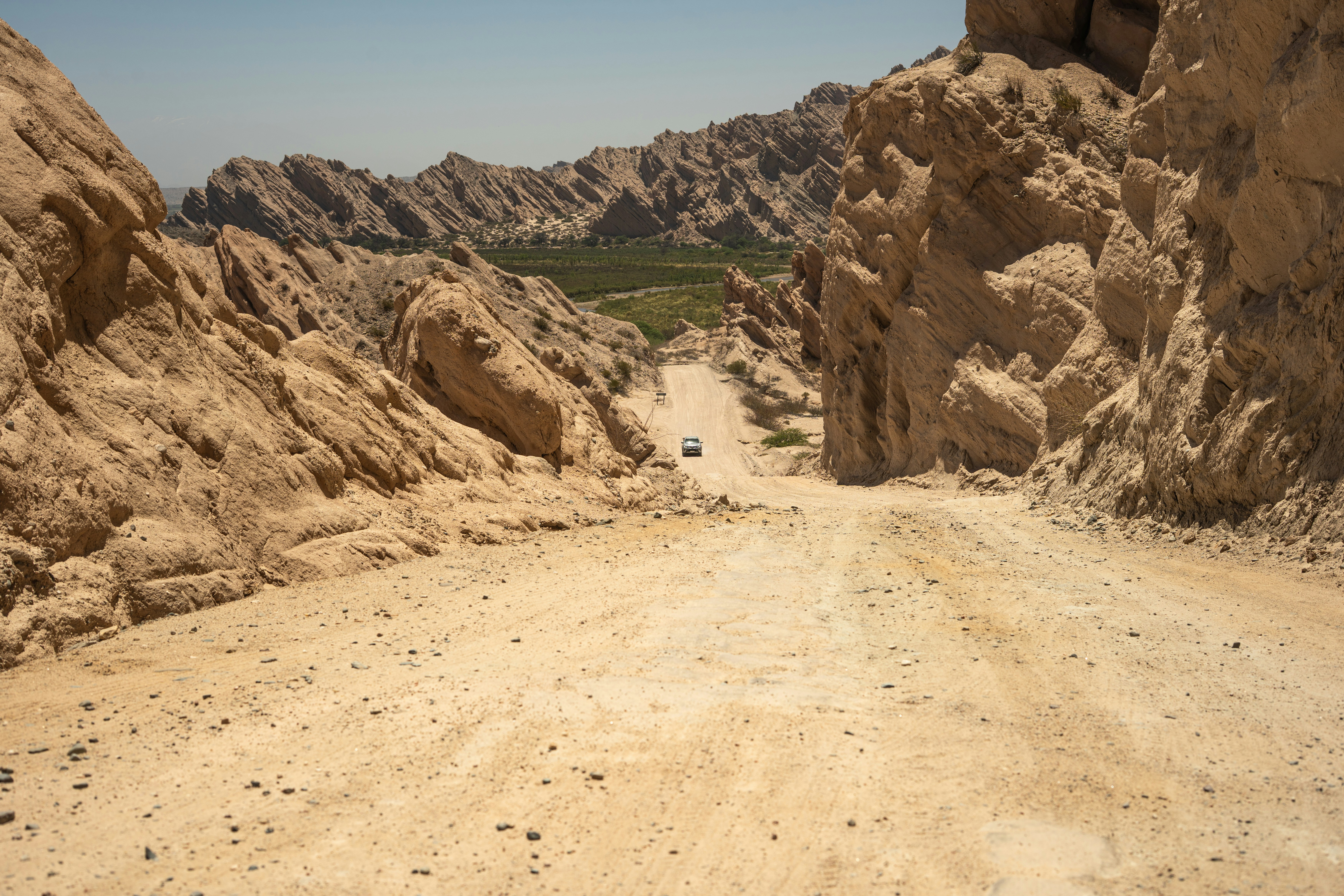 Long straight gravel road stretching through pale desert fields into distant peaks.