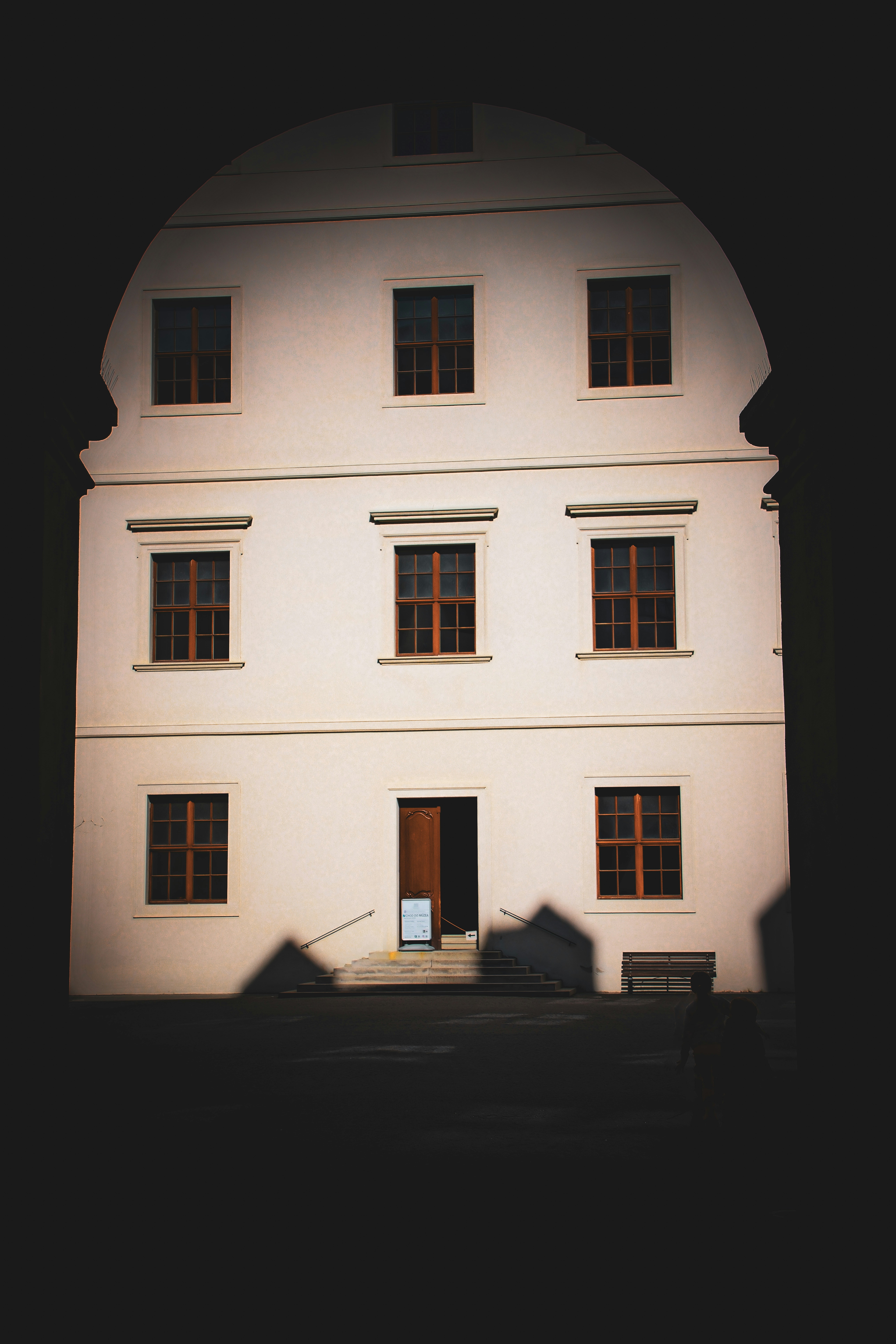A symmetrical building facade is framed by a dark archway, creating a dramatic contrast between light and shadow.