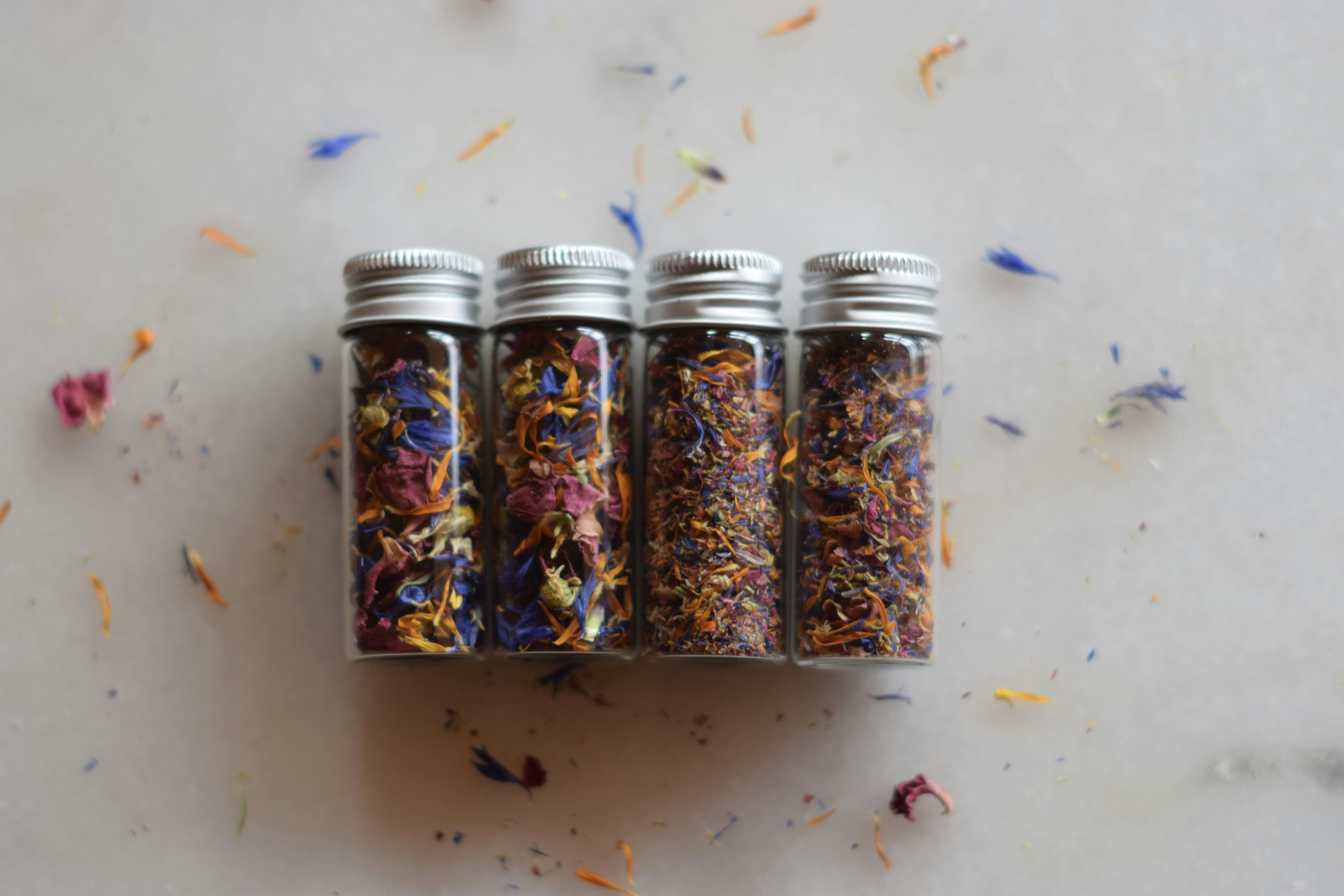 Four vials of dried petals on a light surface