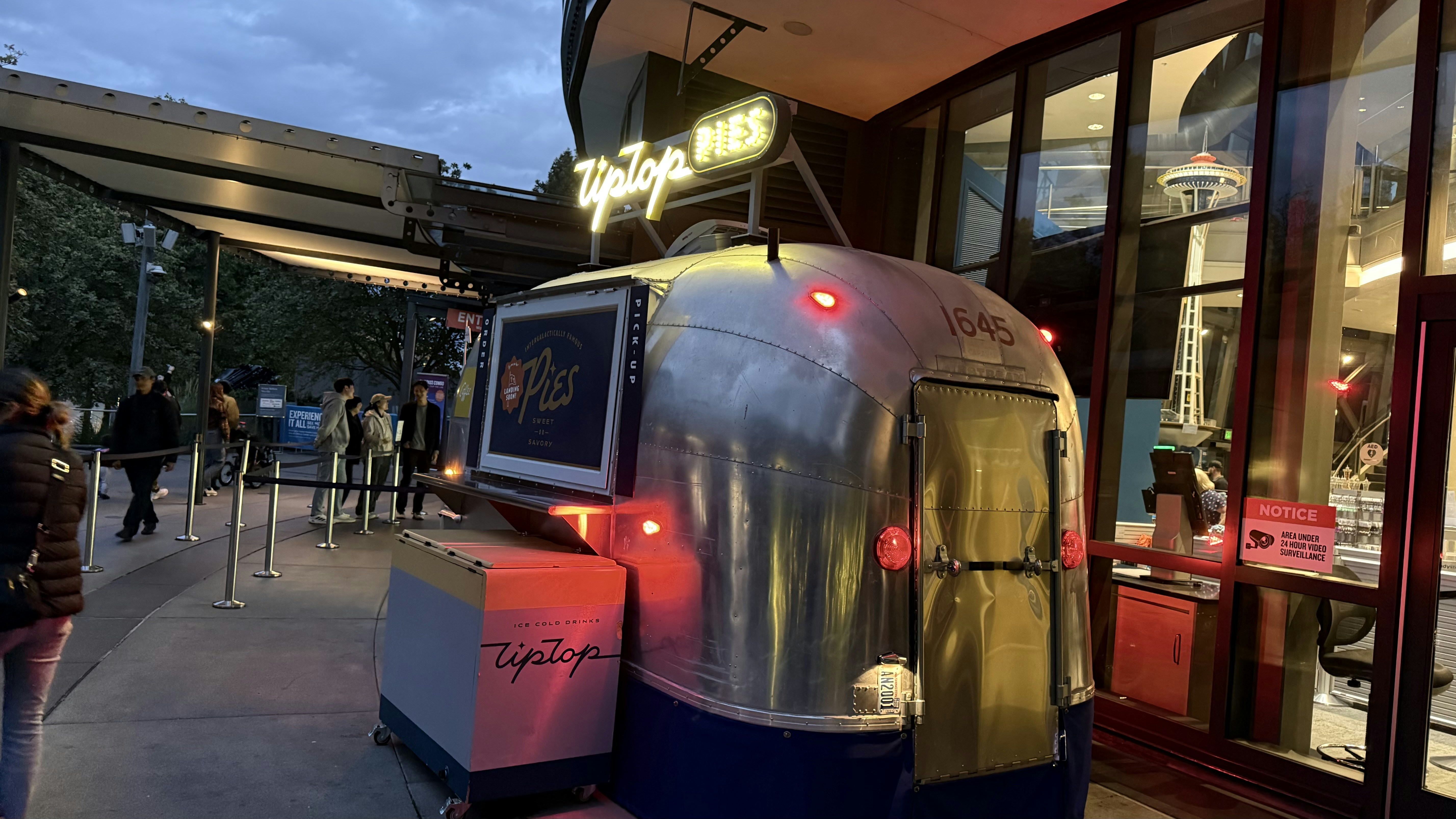Airstream storefront glow: neon and people at dusk