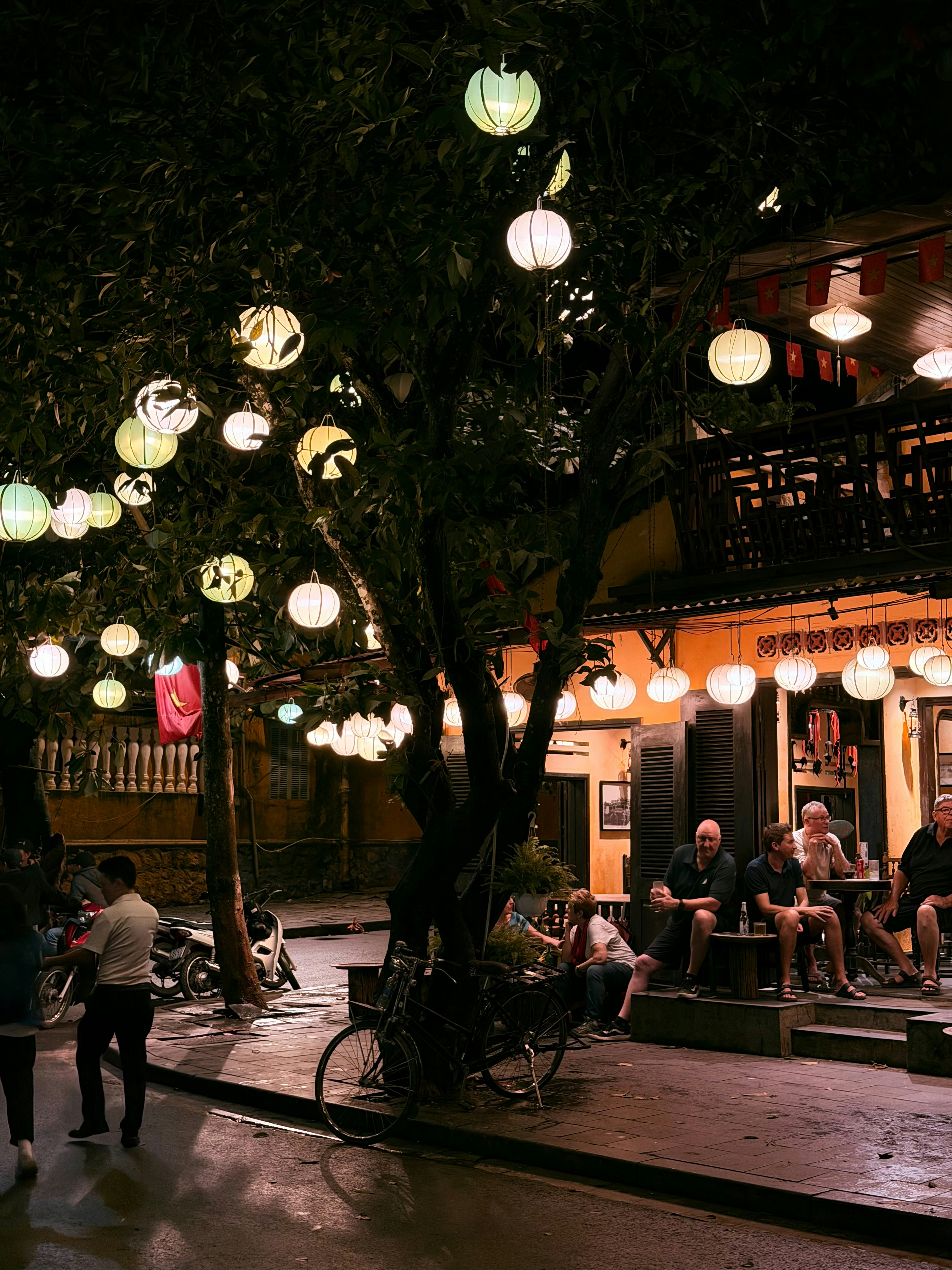 Paper lanterns illuminate a street cafe at night.