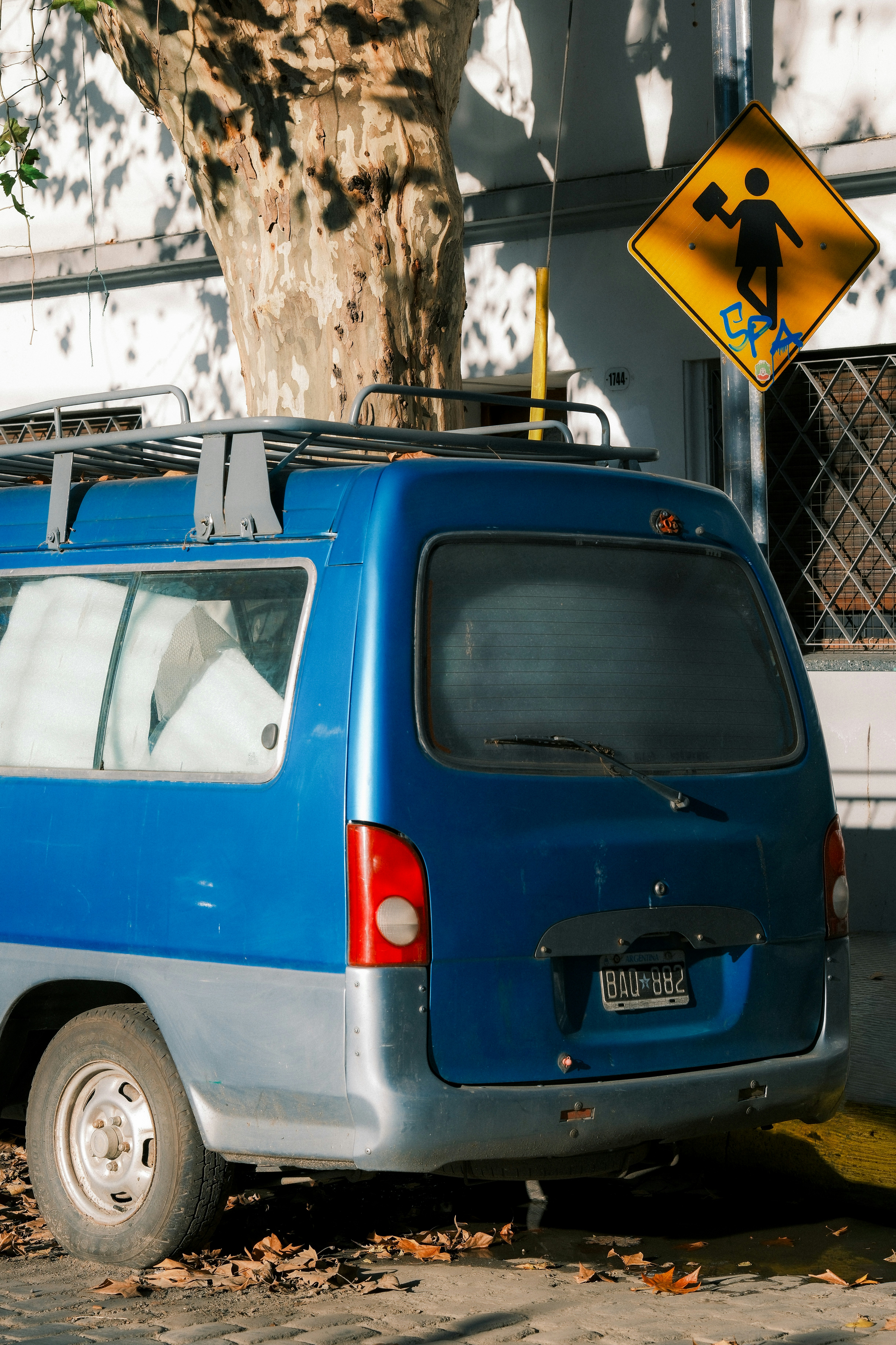 Blue van under a caution sign: street scene with a sunny tree