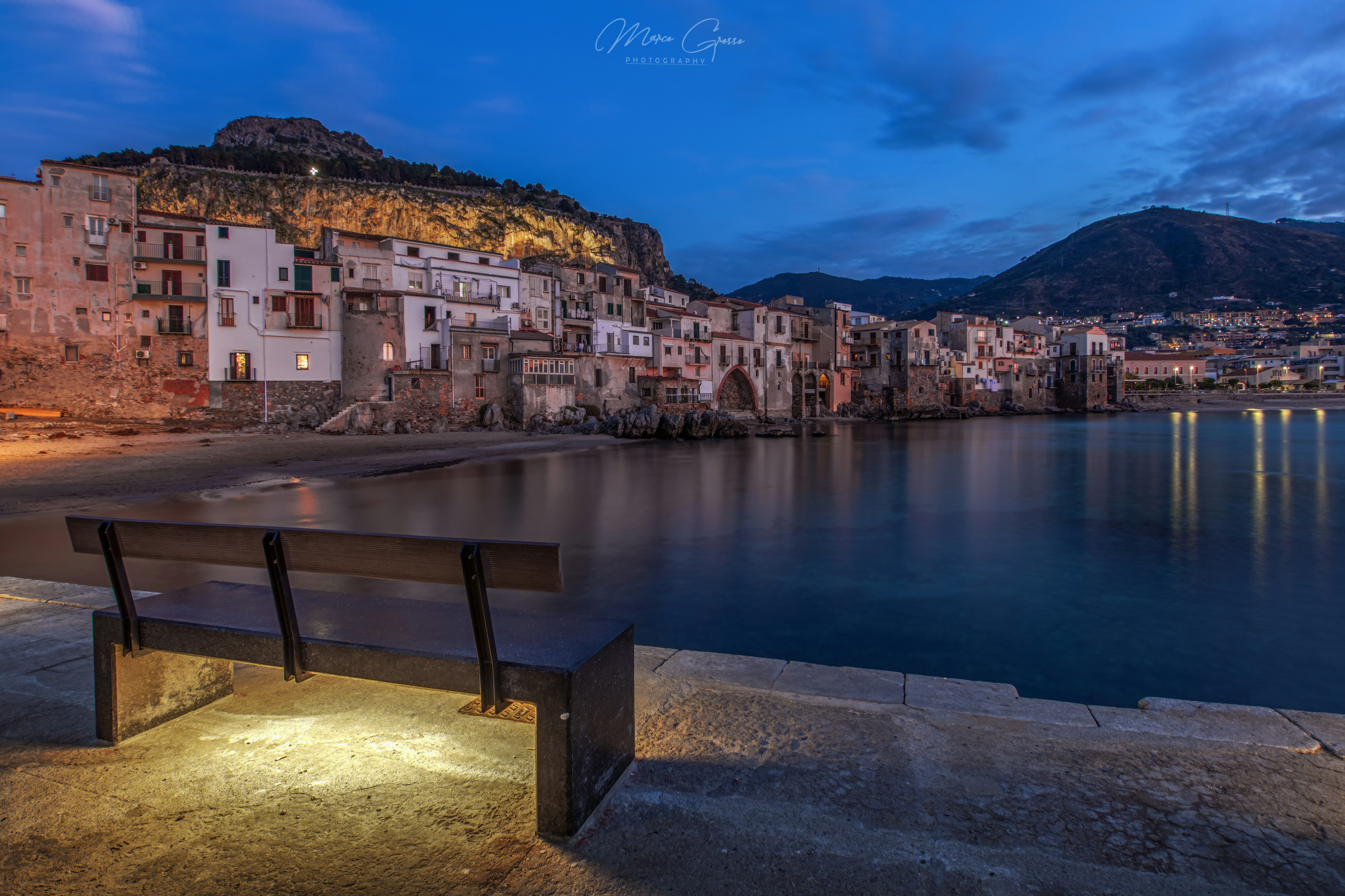 Moonlit harbor village: calm water, warm quay glow