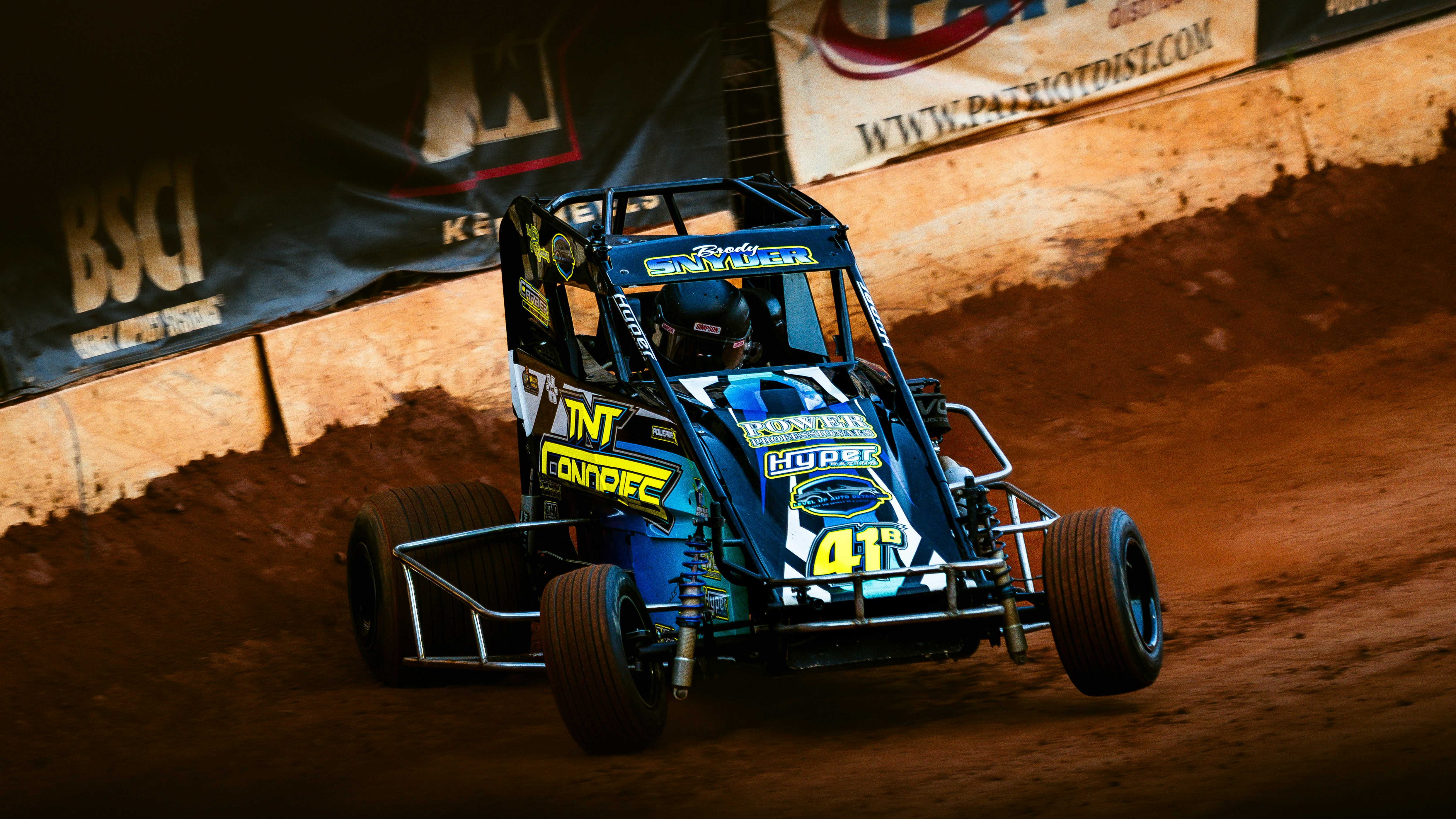 Blue sprint: a dirt-track sprint car powers through a corner under warm arena lights