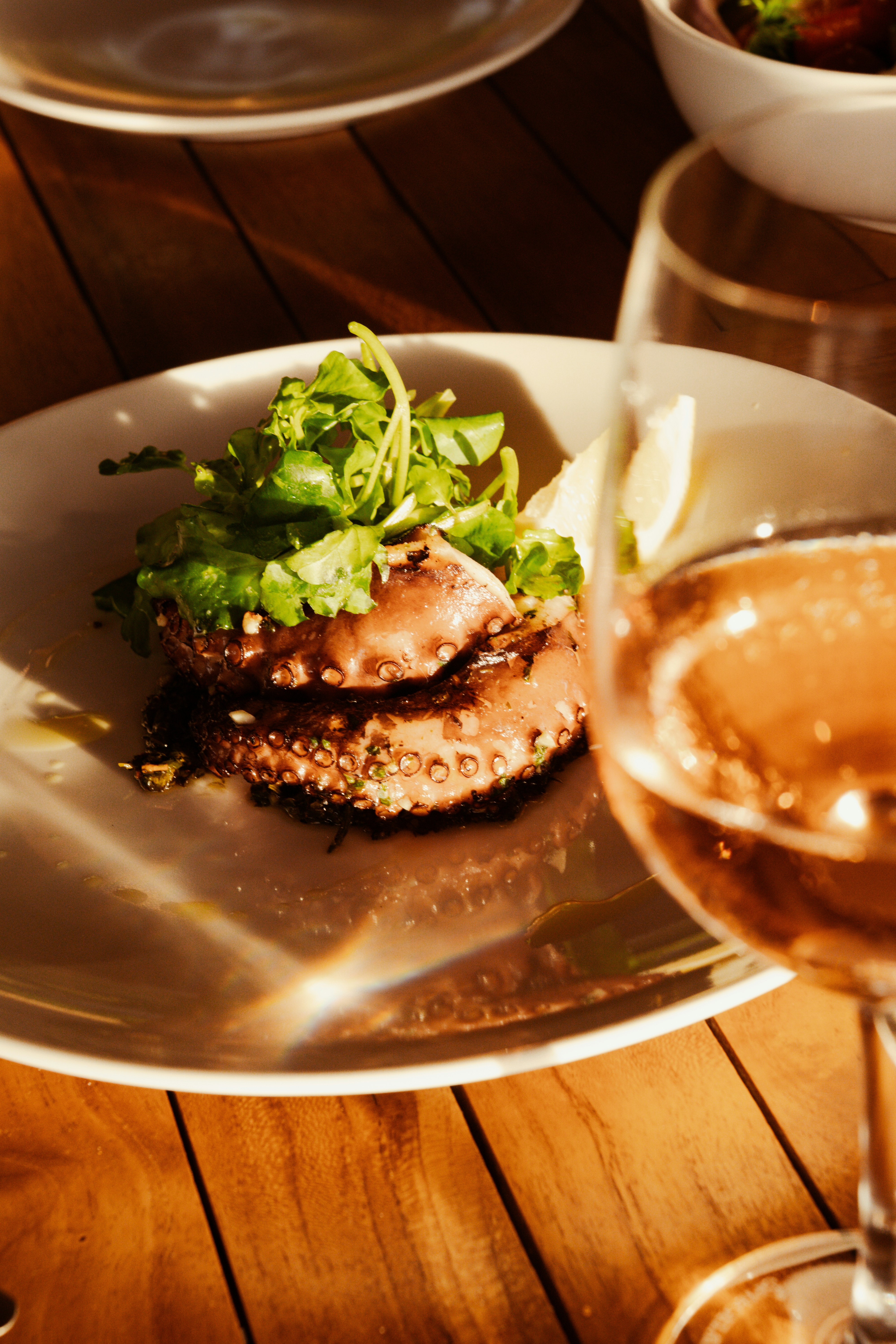 Charred octopus with greens and citrus on a warm wood table