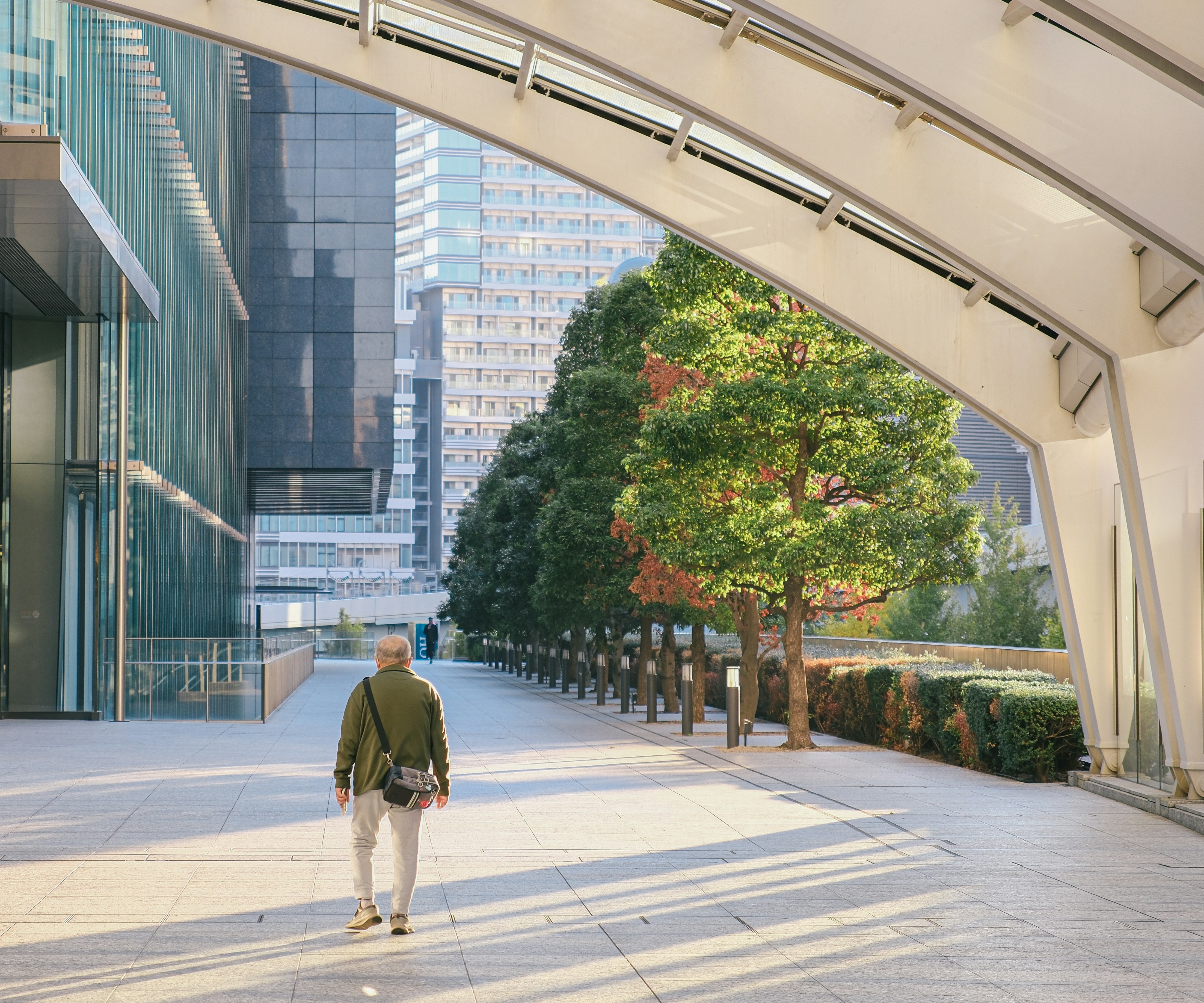 Pedestrian in a sunlit urban plaza framed by modern architecture