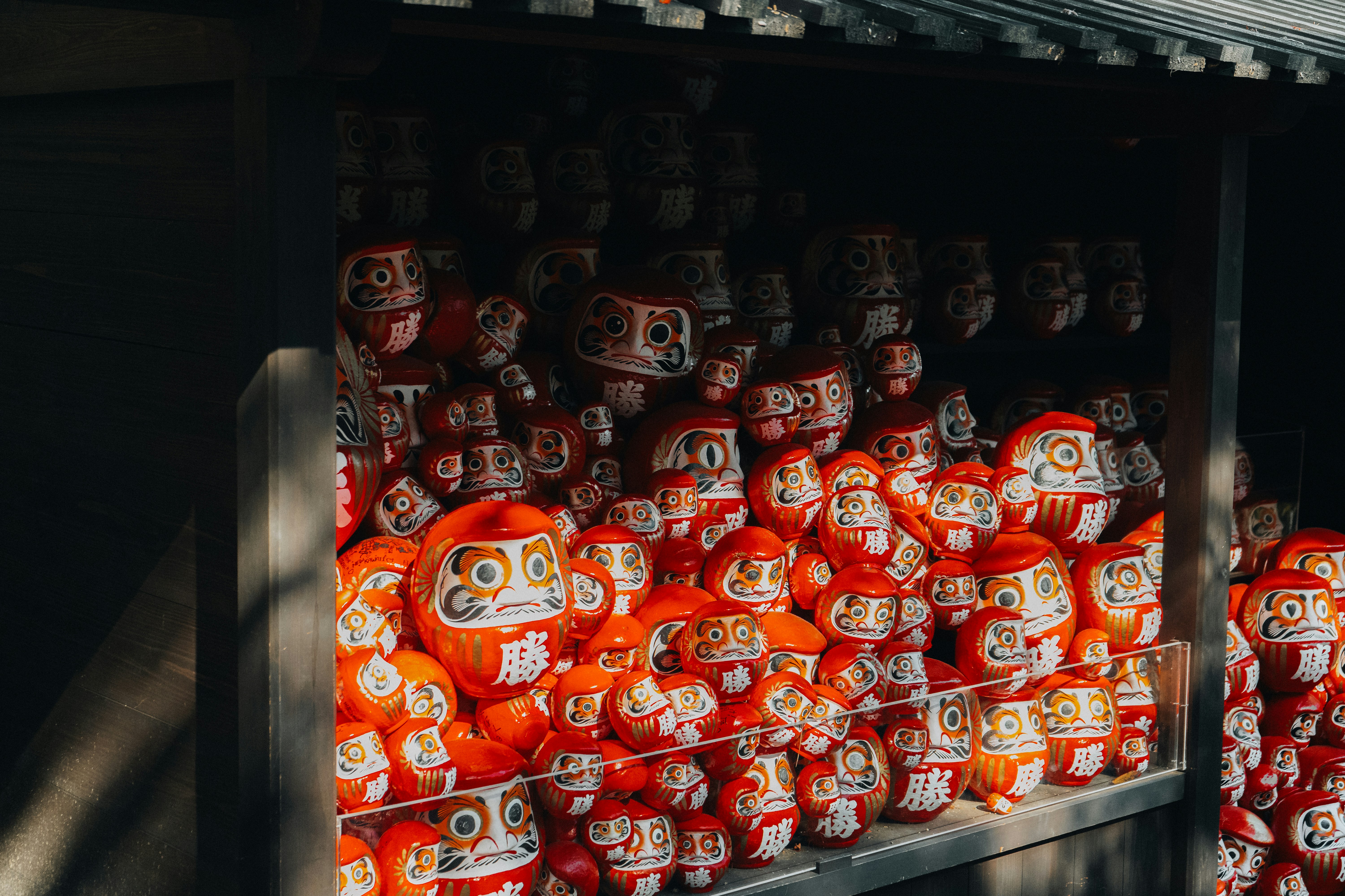 A Sea of Daruma Eyes: Red Whimsy in Shadowed Shelves