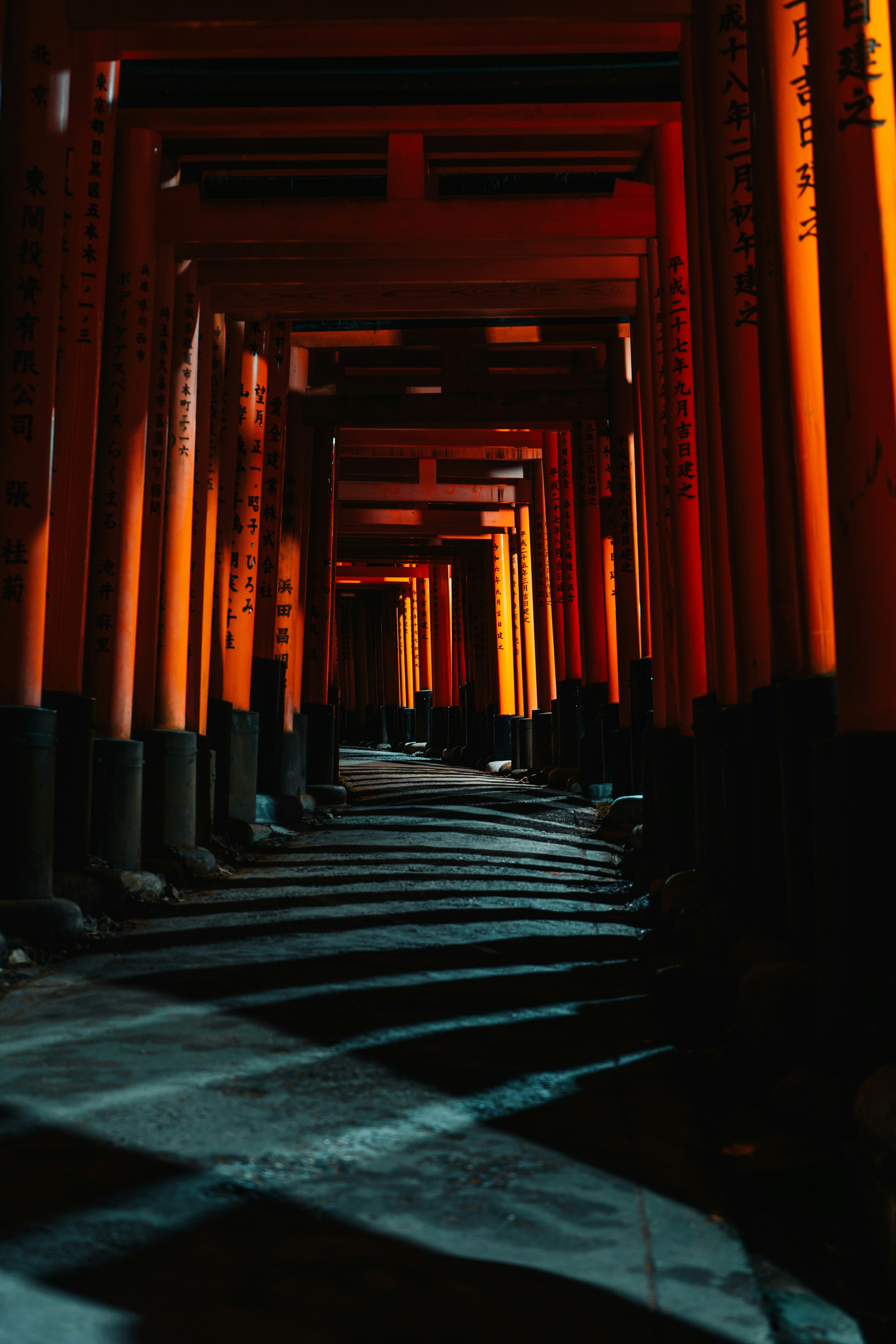 A night shot of the famous torii gate pathway at Fushimi Inari Shrine in Kyoto, Japan. The long corridor of vermilion gates is softly lit, highlighting the textures, shadows, and depth of the historic shrine path.
