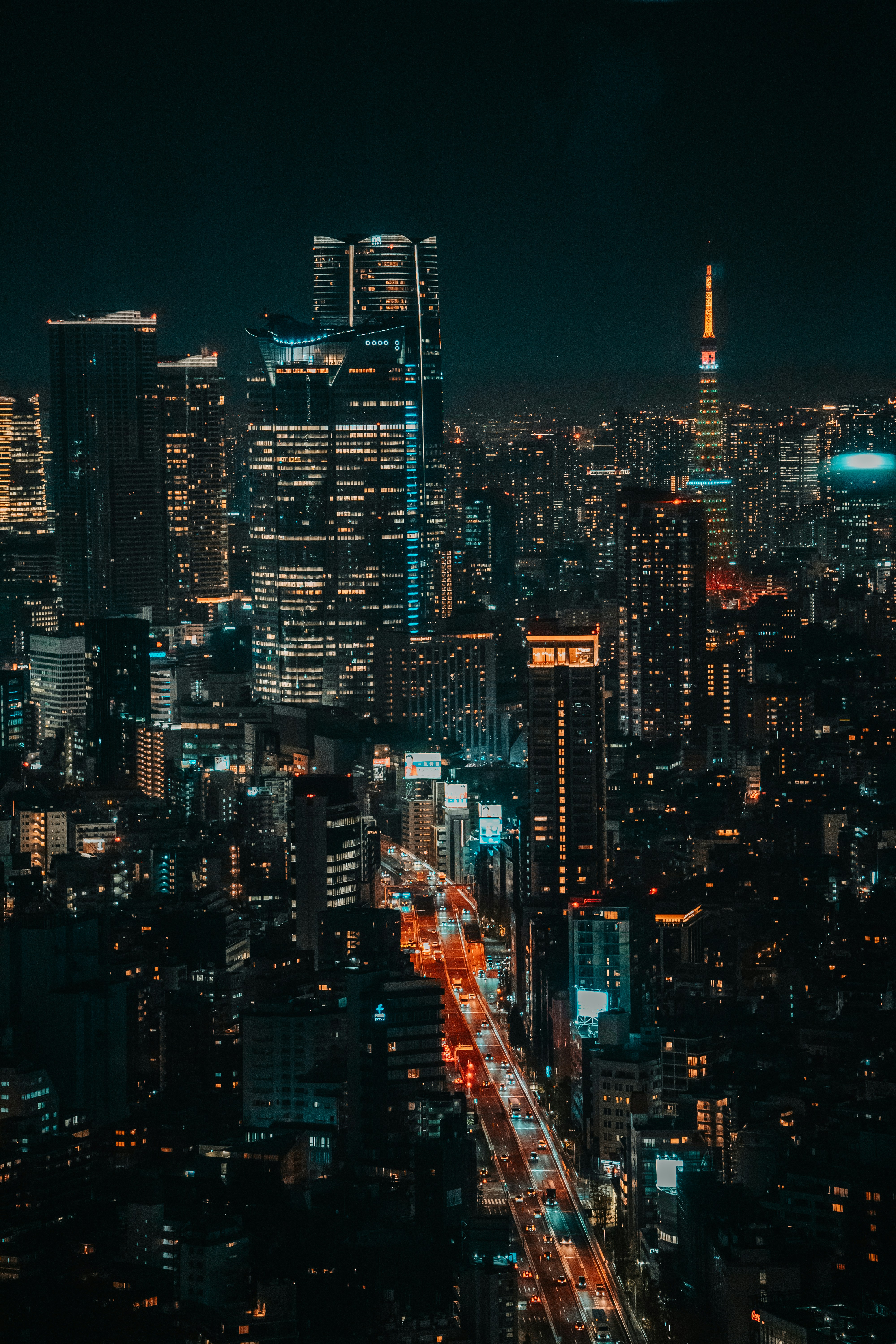 A high-angle night photograph of Shibuya Crossing in Tokyo, Japan, taken from a skyscraper. The scene highlights vibrant neon lights, dense urban architecture, and the movement of crowds and traffic below.