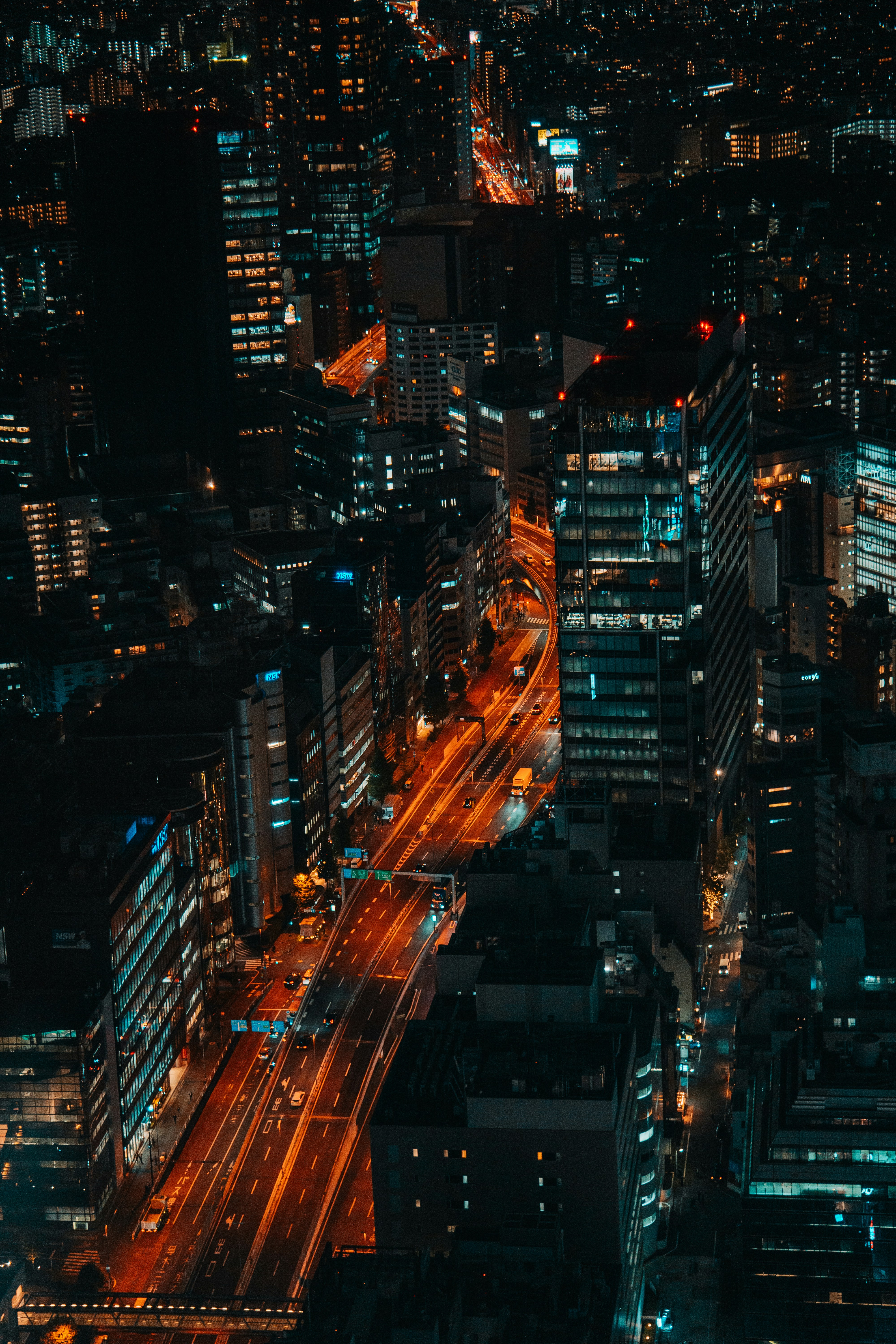 A high-angle night photograph of Shibuya Crossing in Tokyo, Japan, taken from a skyscraper. The scene highlights vibrant neon lights, dense urban architecture, and the movement of crowds and traffic below.