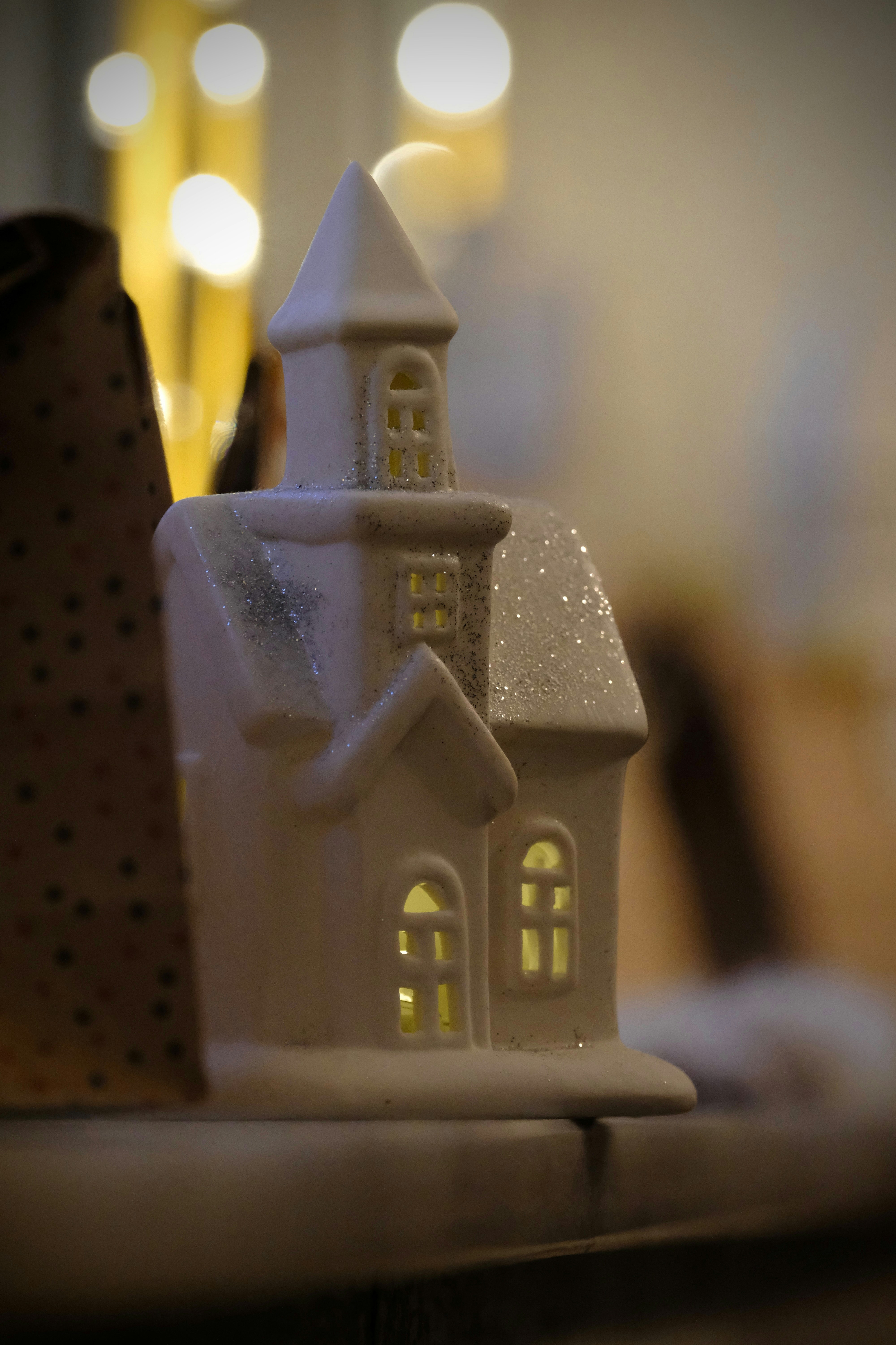 Glowing Hearth: A Tiny Ceramic Church Between Christmas Lights