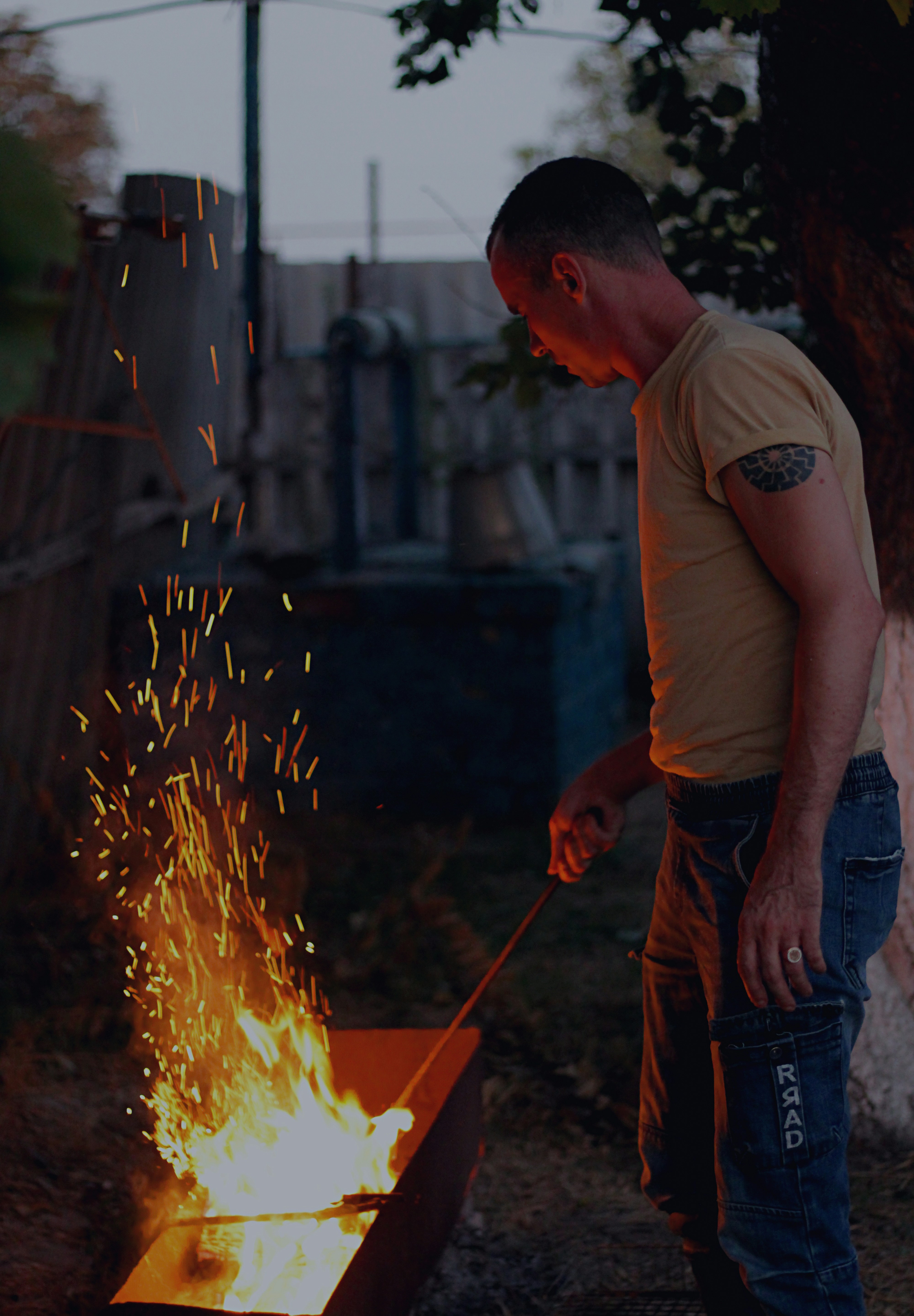 Industrial Ember: a man tending a forge under dusk glow