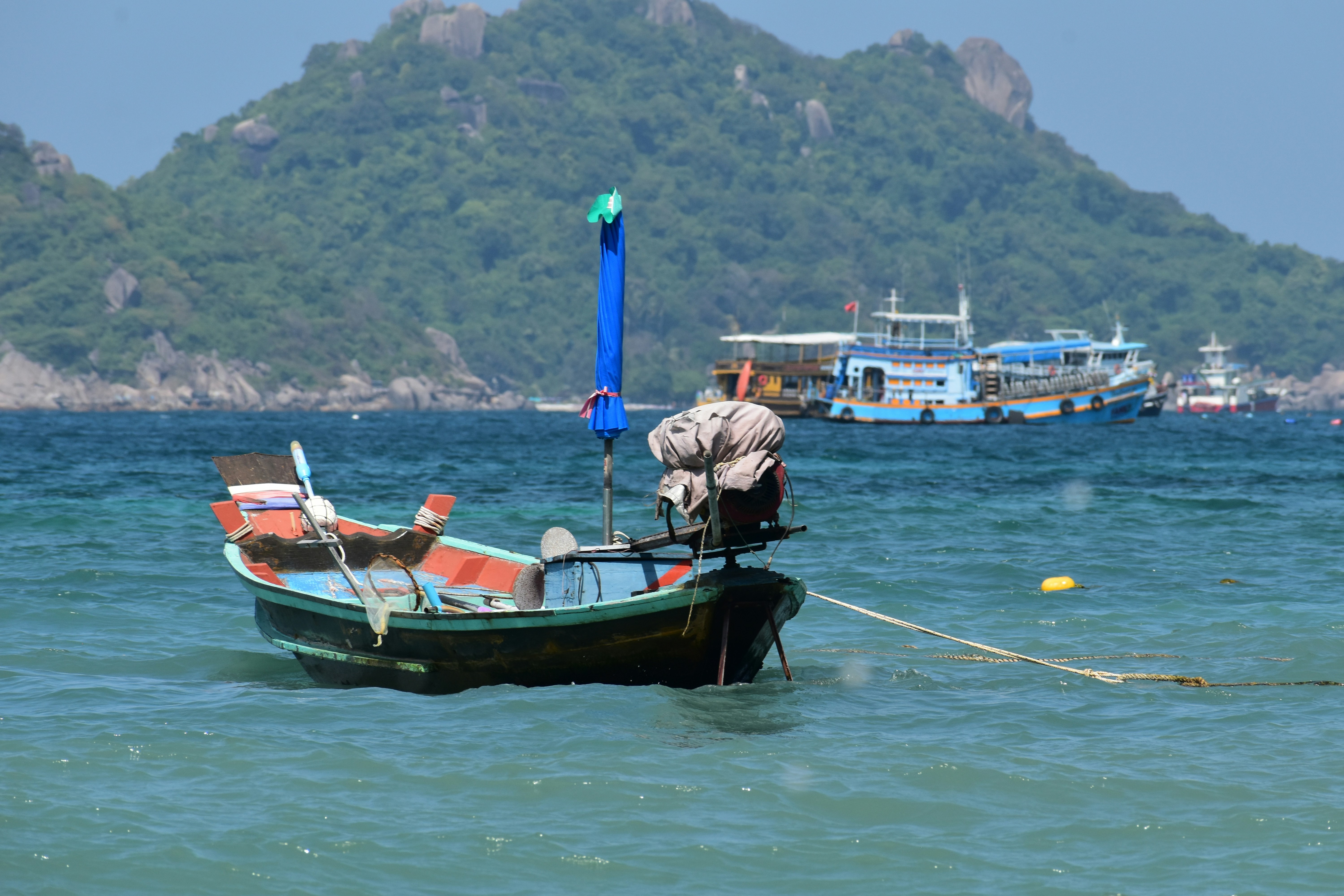 Boat in turquoise bay with distant cargo vessel and green island backdrop
