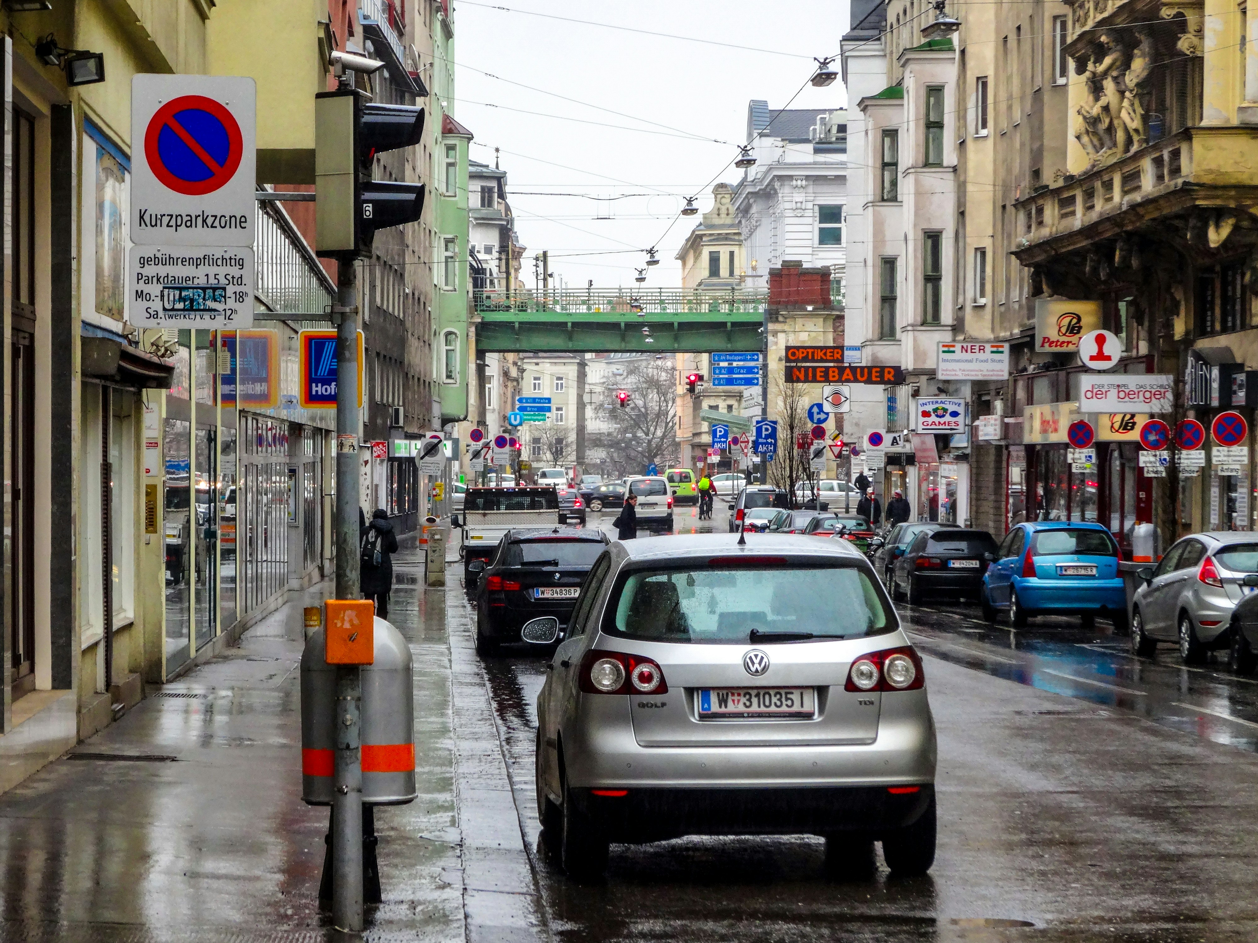 Rain-Slicked City Corridor: Cars, Signs, and a Glimmering Overpass