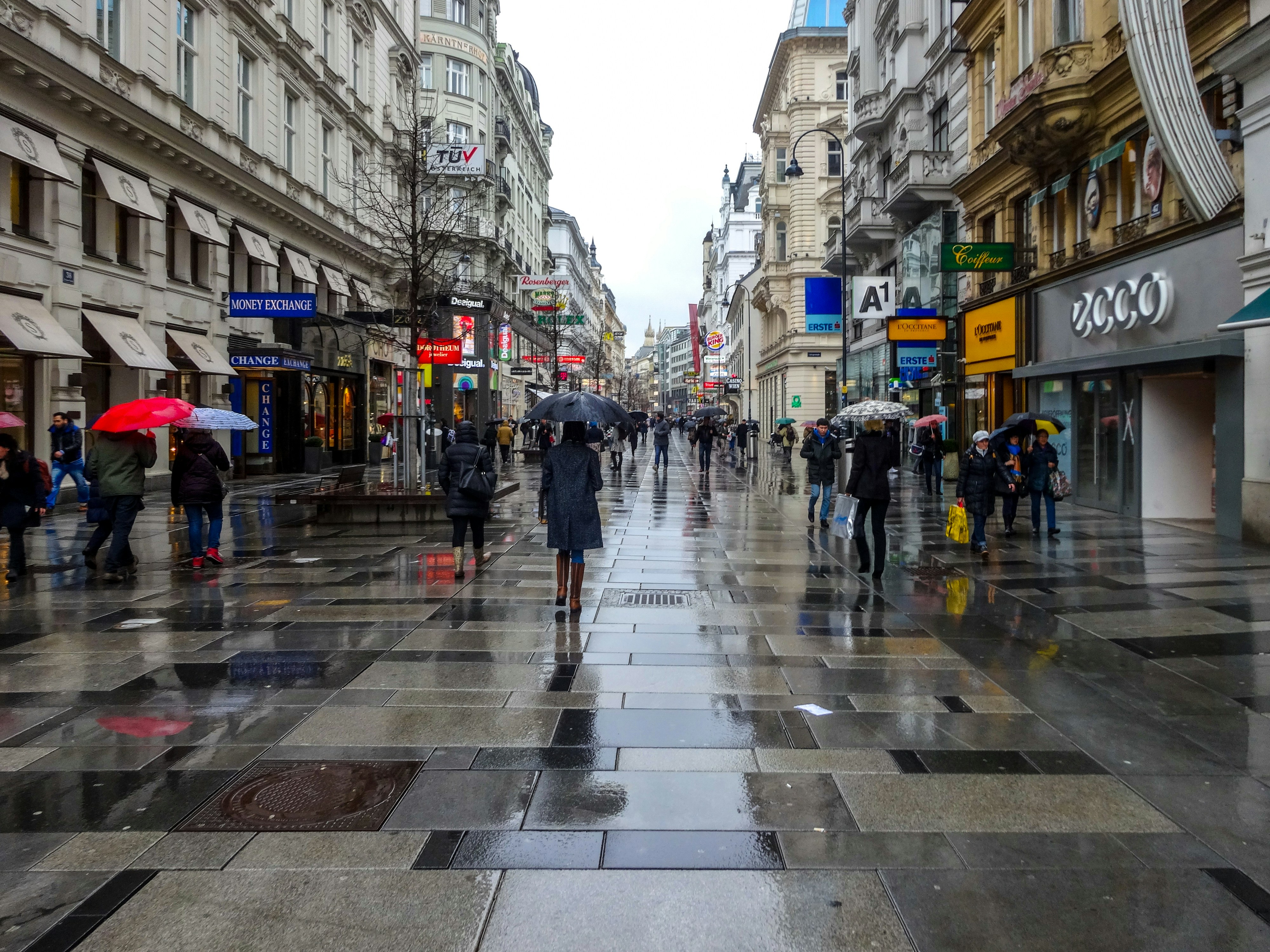 People with umbrellas walk on wet city street