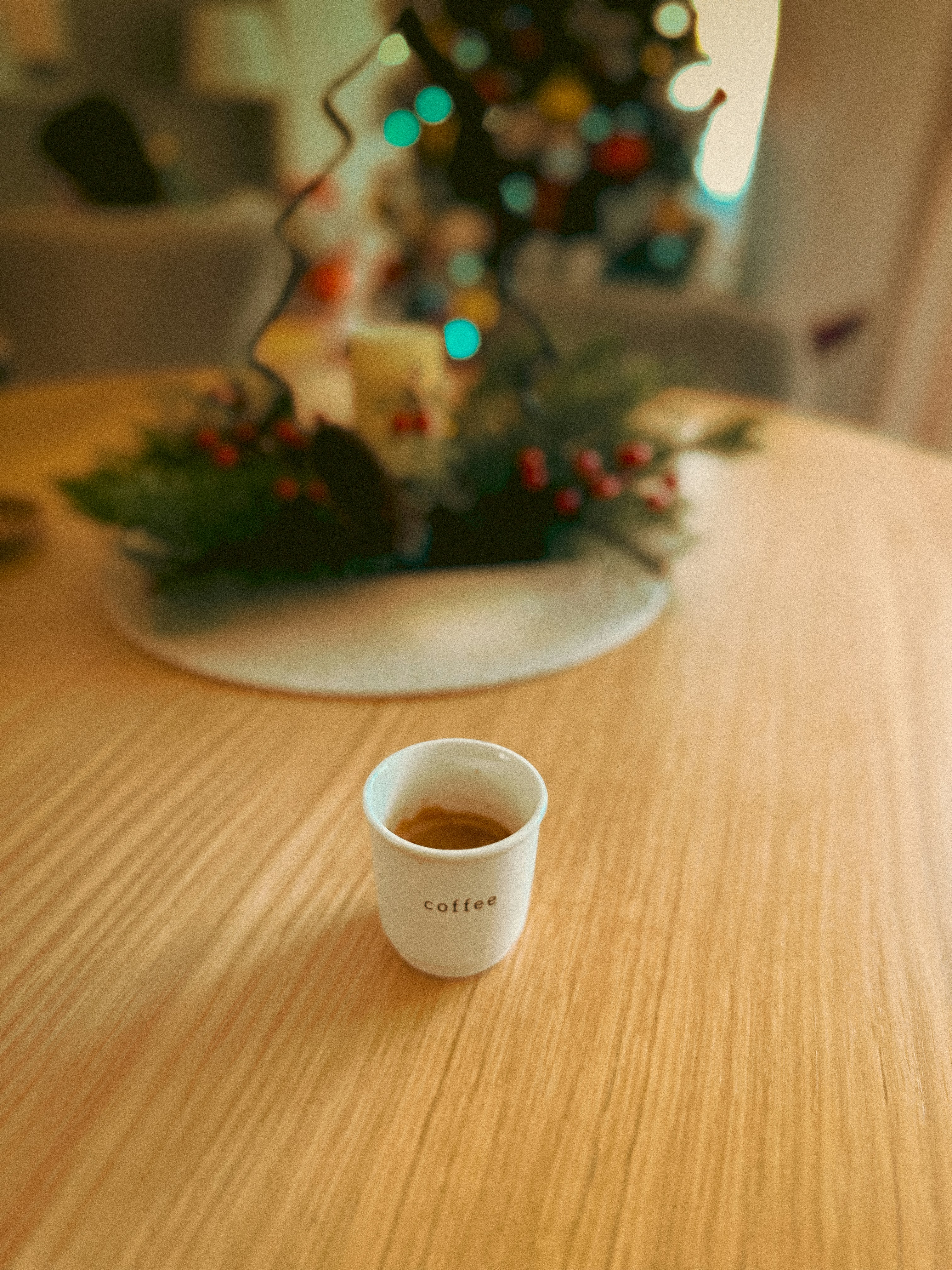 A small espresso cup on a wooden table with a soft holiday background and warm bokeh.