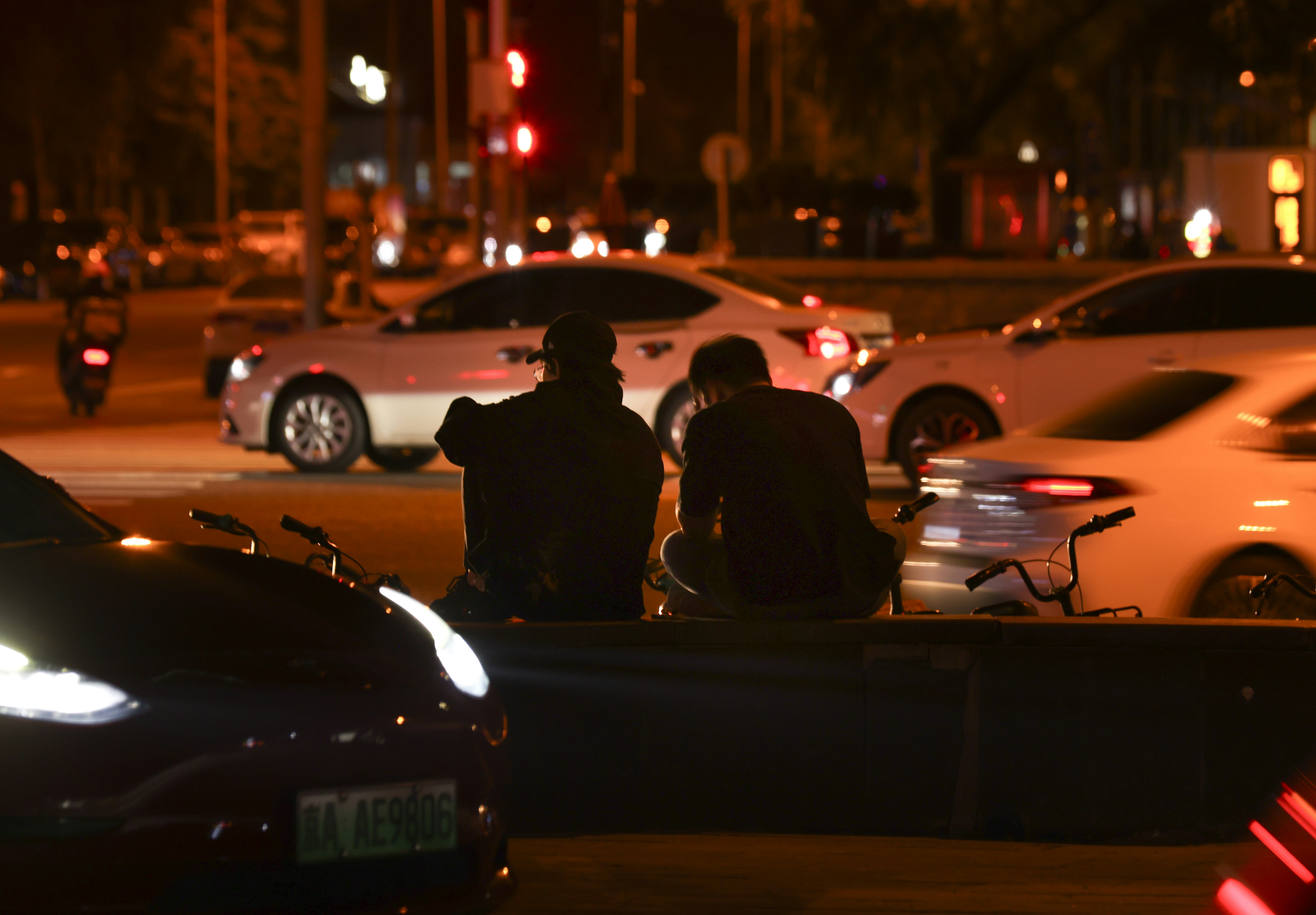 Two silhouettes on a night-city bench watching traffic glow