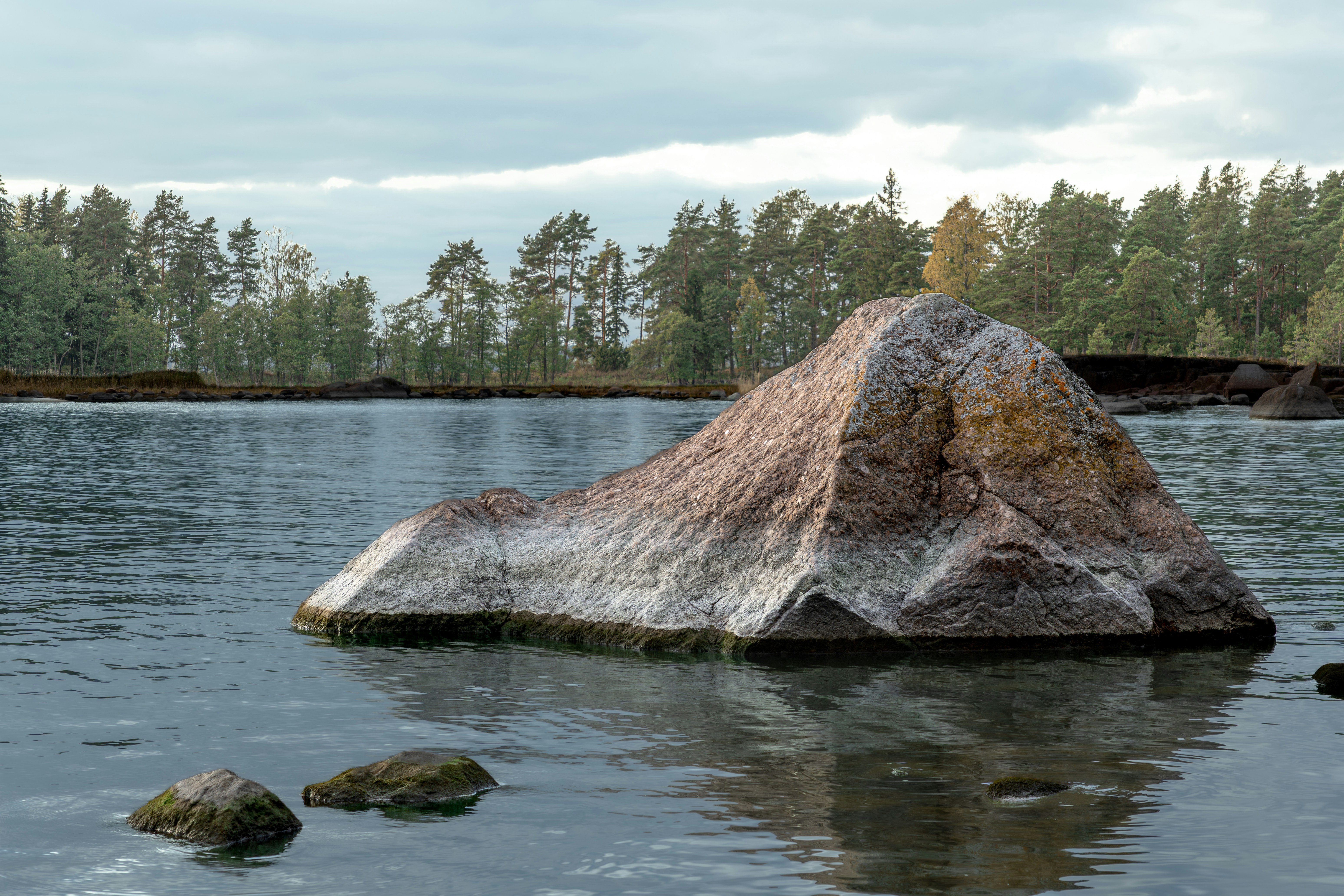 Large rock in calm water with trees behind