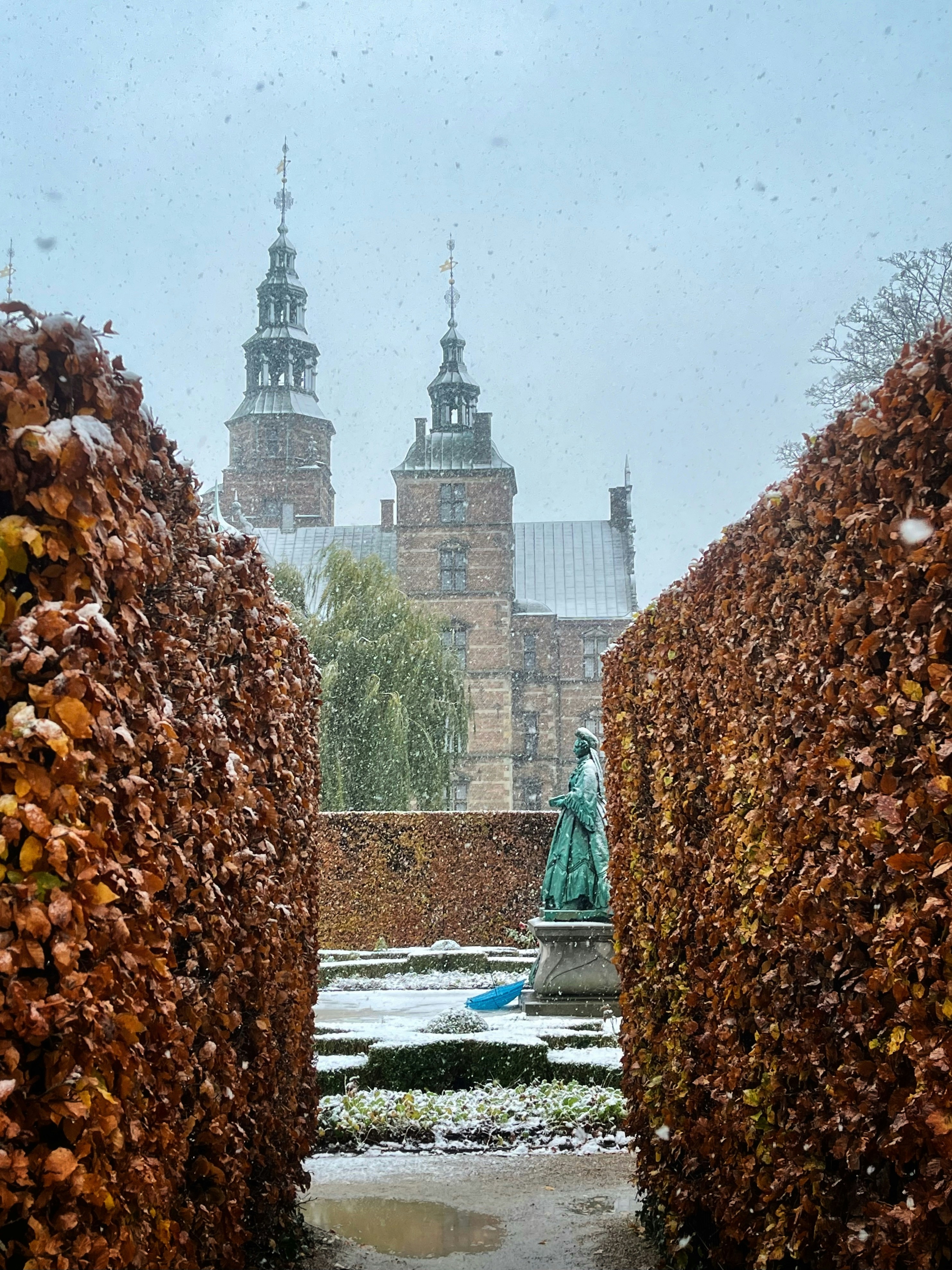 Statue Garden in Snow: Framed by Autumn Hedges with Historic Towers Peeking Through