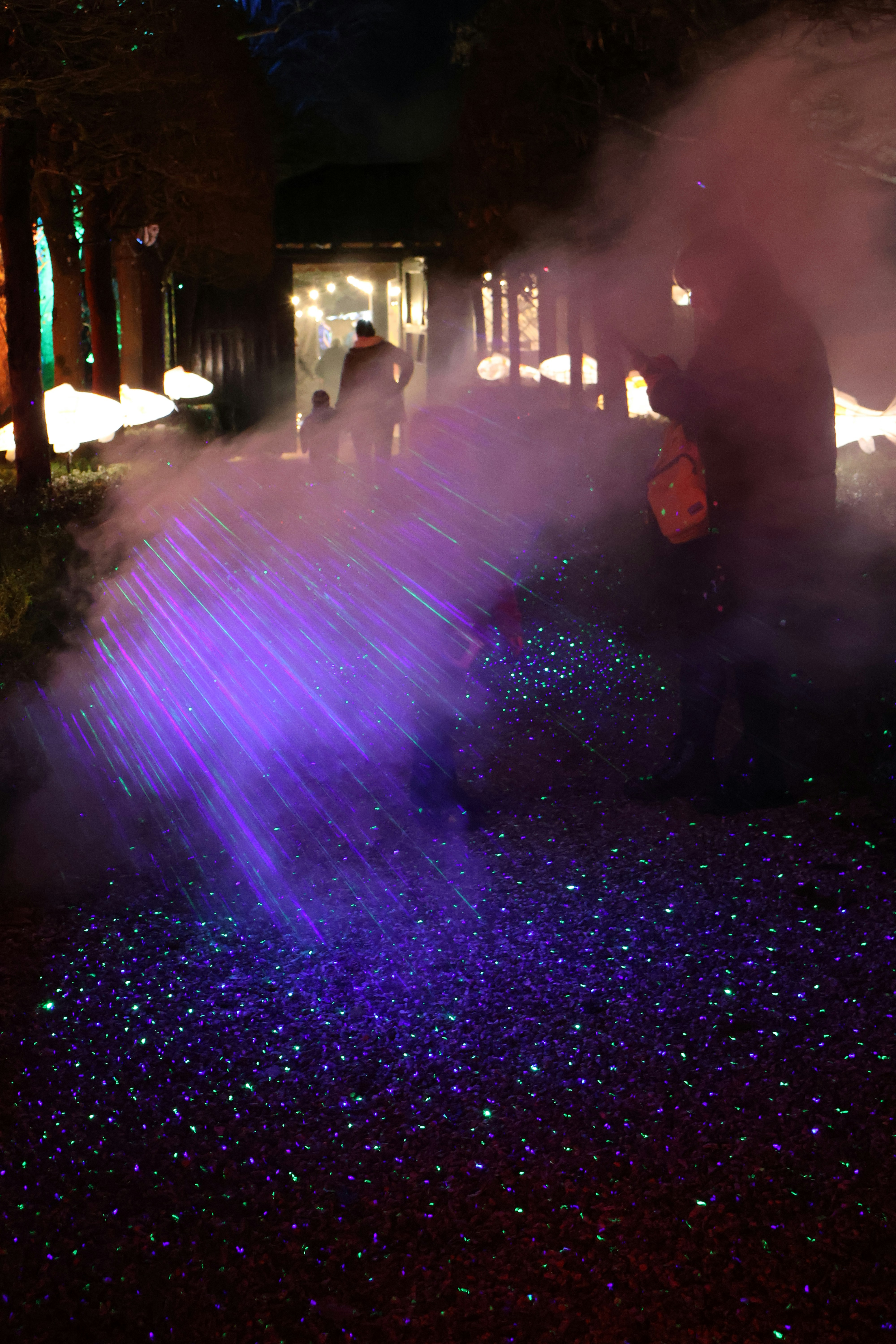 Purple and green lights illuminate smoky ground at night.