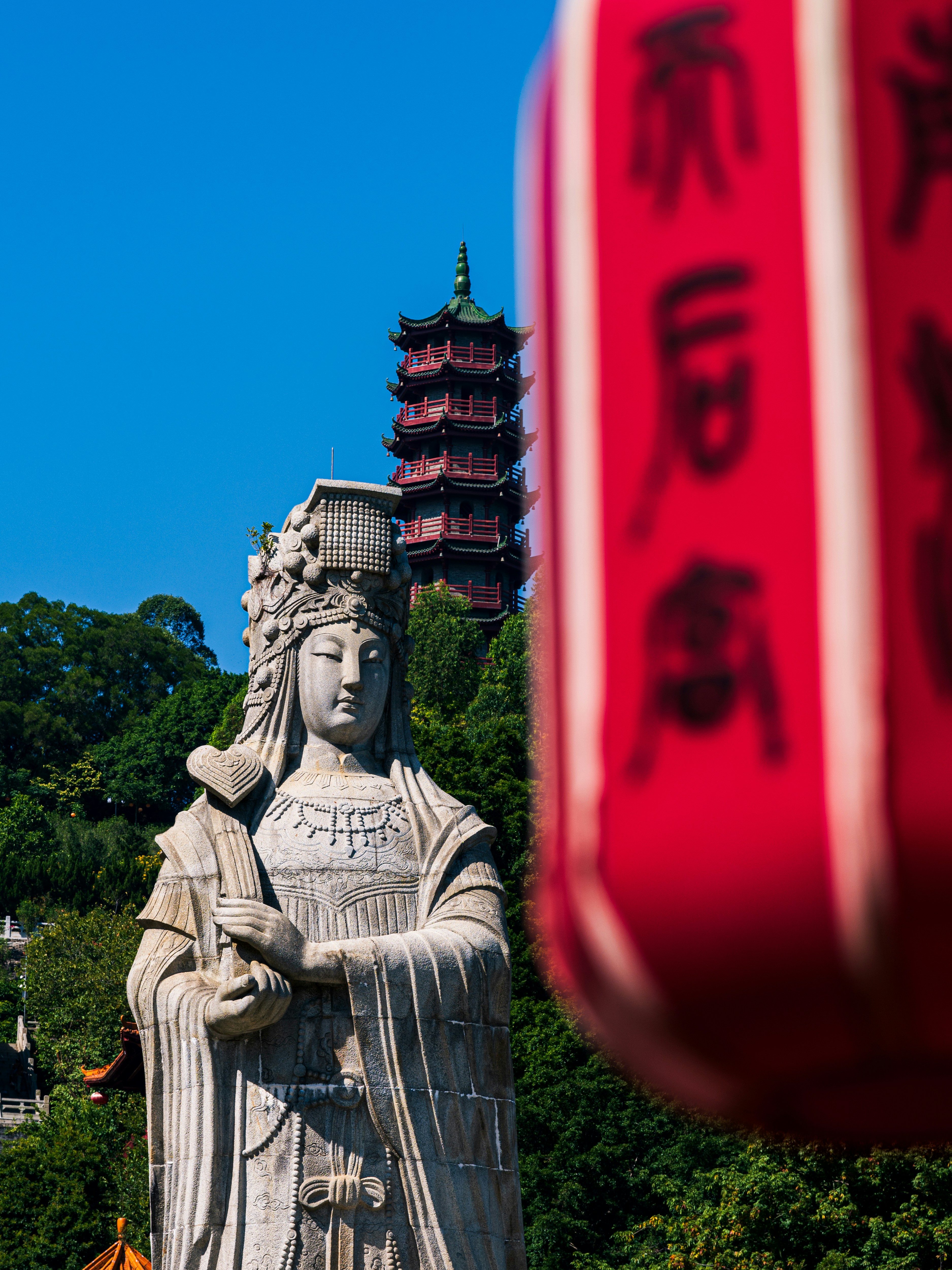 Guardians of the Peak: A Stone Statue Framed by Red Lanterns and a Pagoda