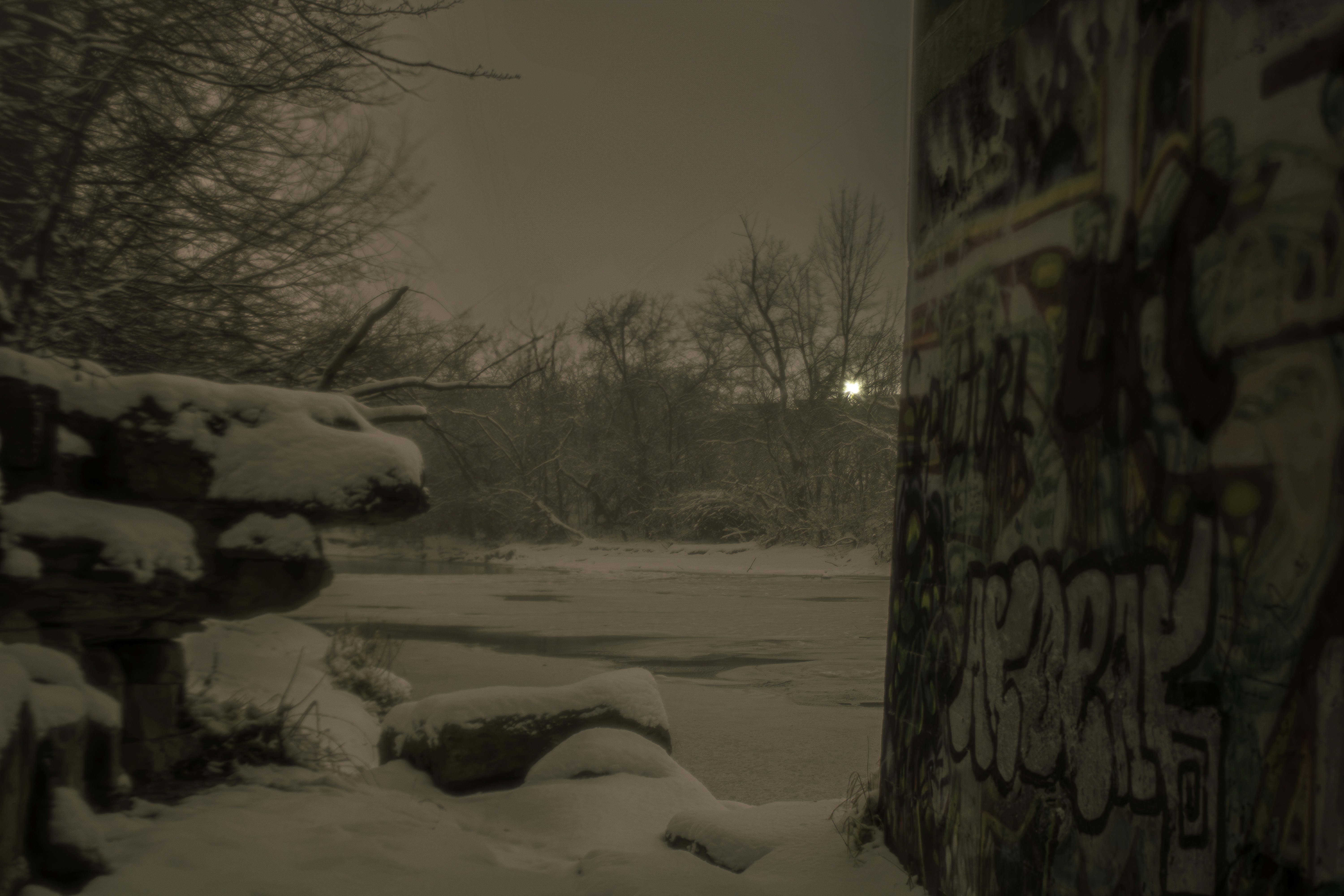 Snowy riverbank under graffiti-drenched overpass at night