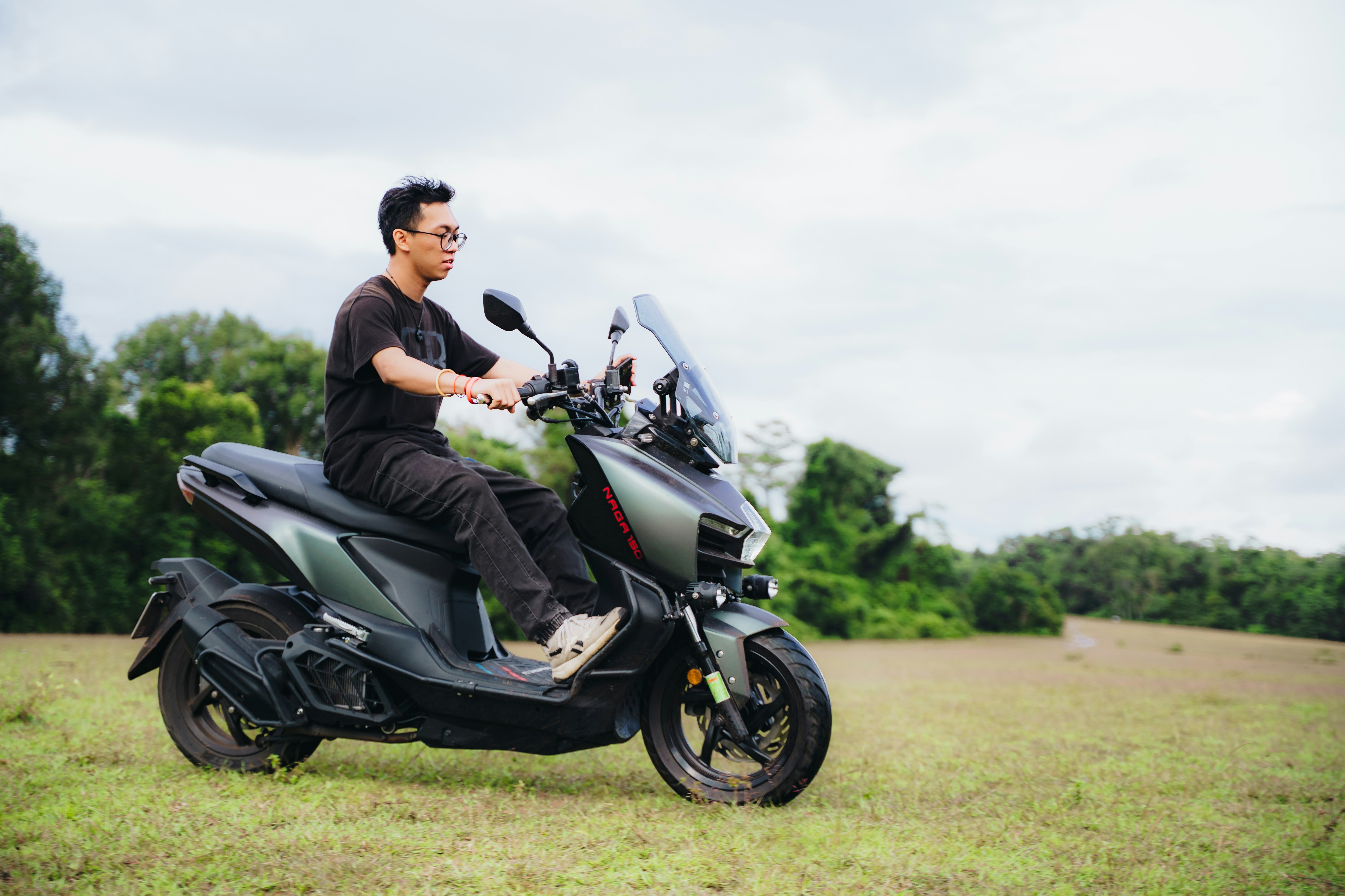 Rider on a matte-black scooter in a sunlit field