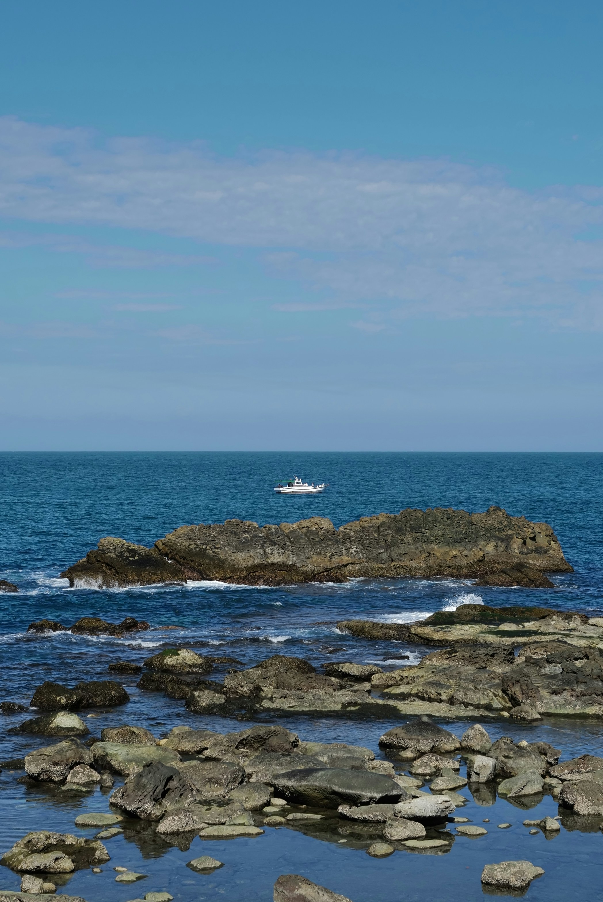 A lone white boat resting on the horizon over a rugged rocky shoreline
