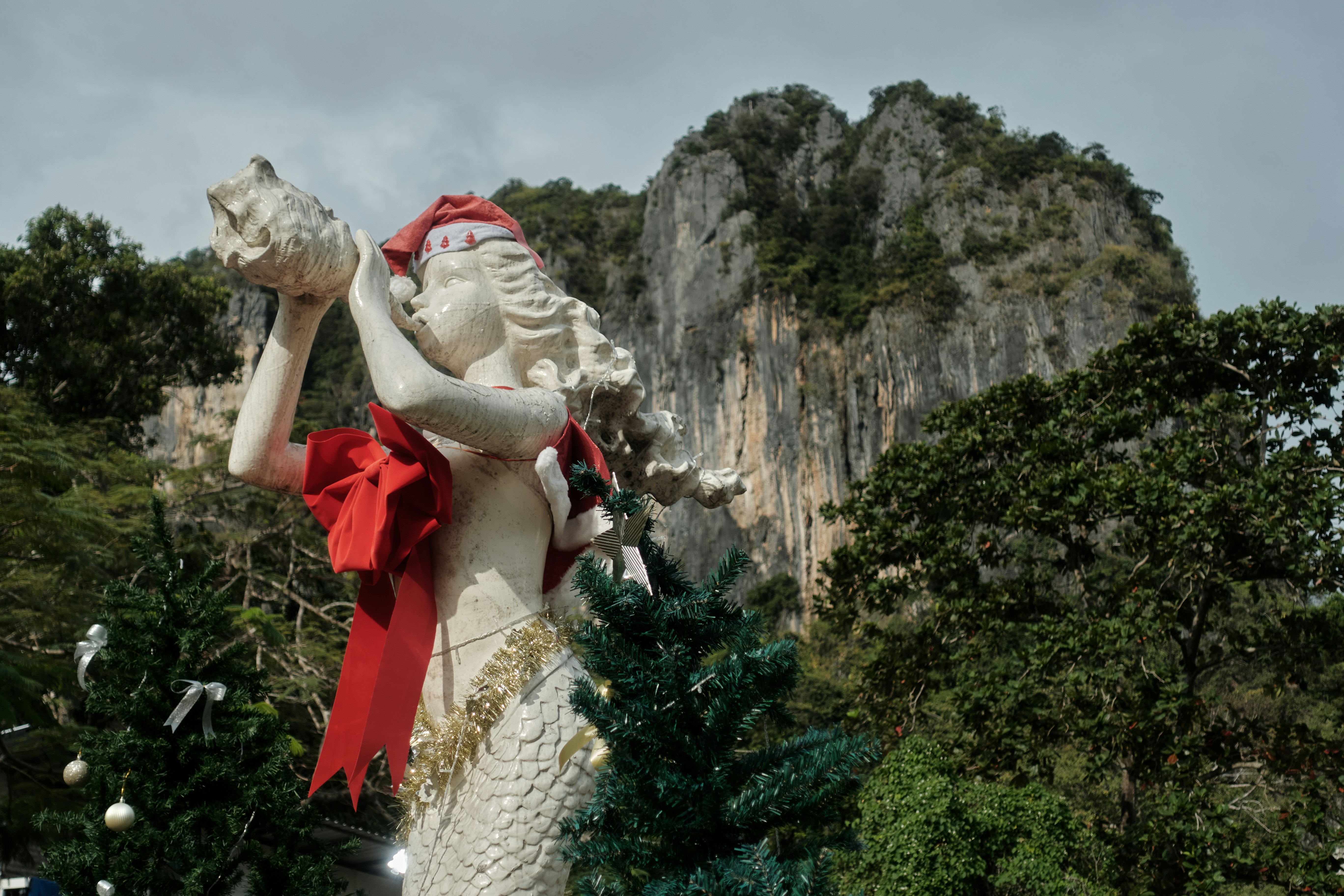 A colossal guardian carries a festive burden beneath a limestone cliff