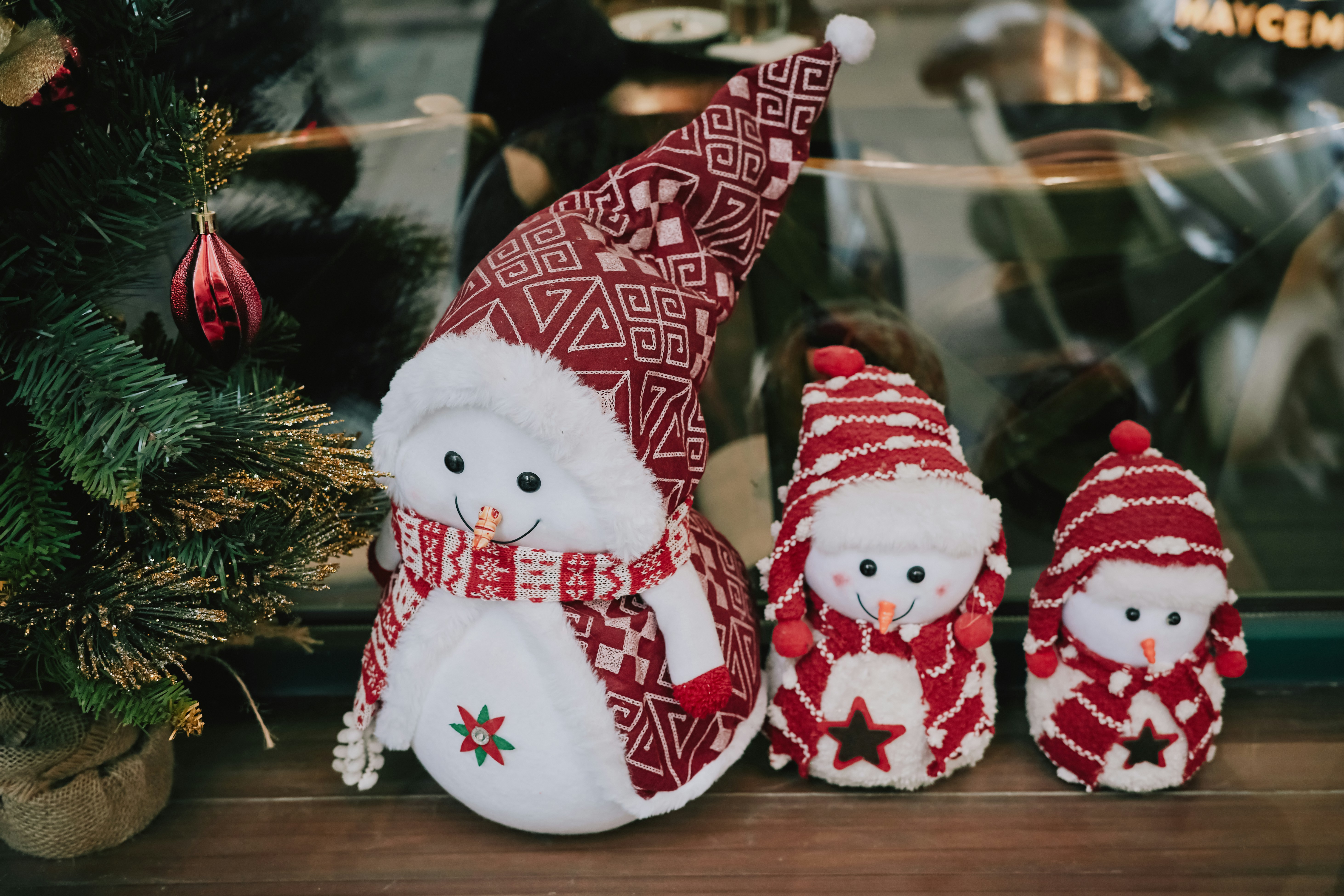 Three festive snowmen stand guard beside a Christmas tree ornamented with red baubles