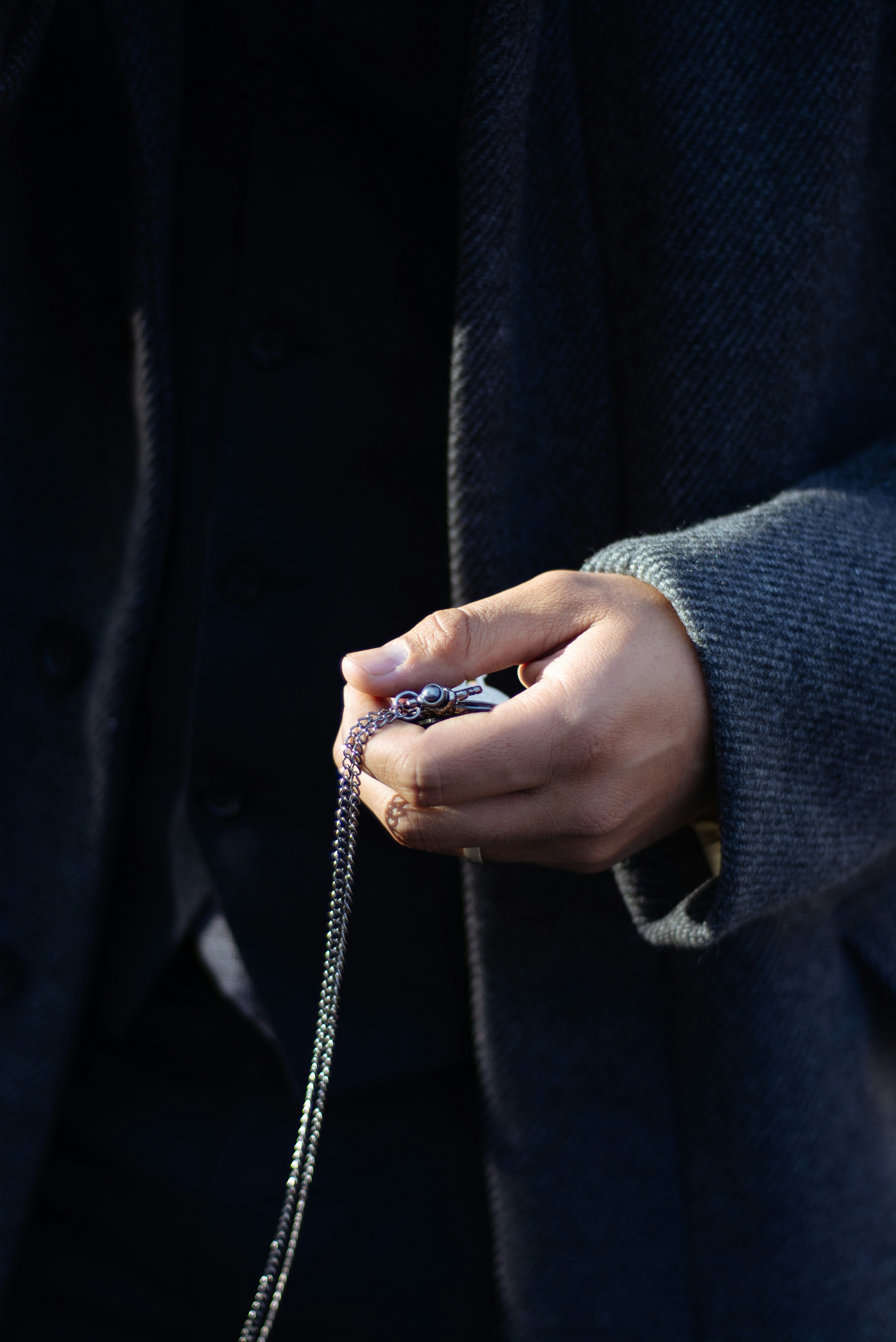 Rusted silver chain slips through a calm hand under a dark coat