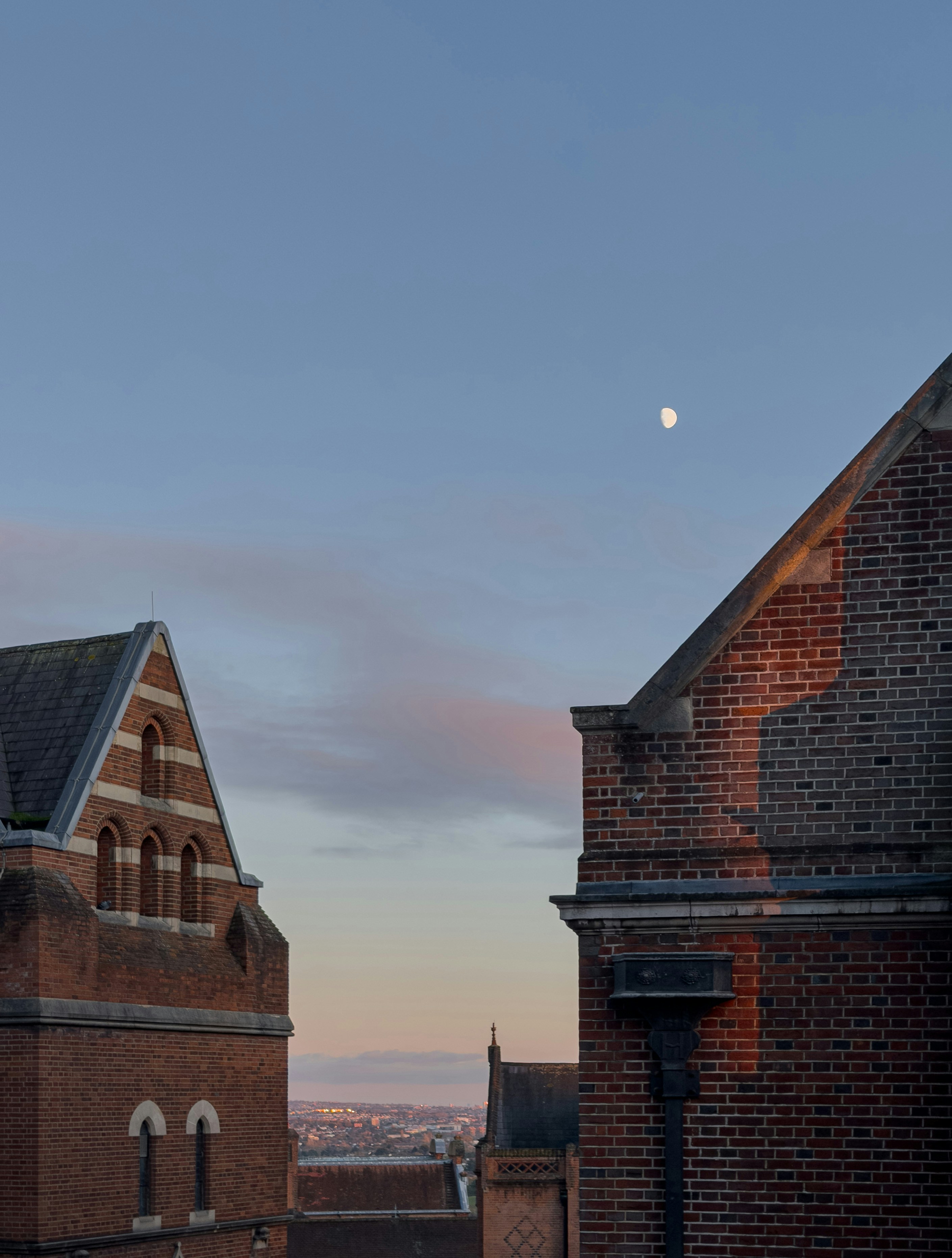 Moon over brick peaks: urban dusk from a rooftop