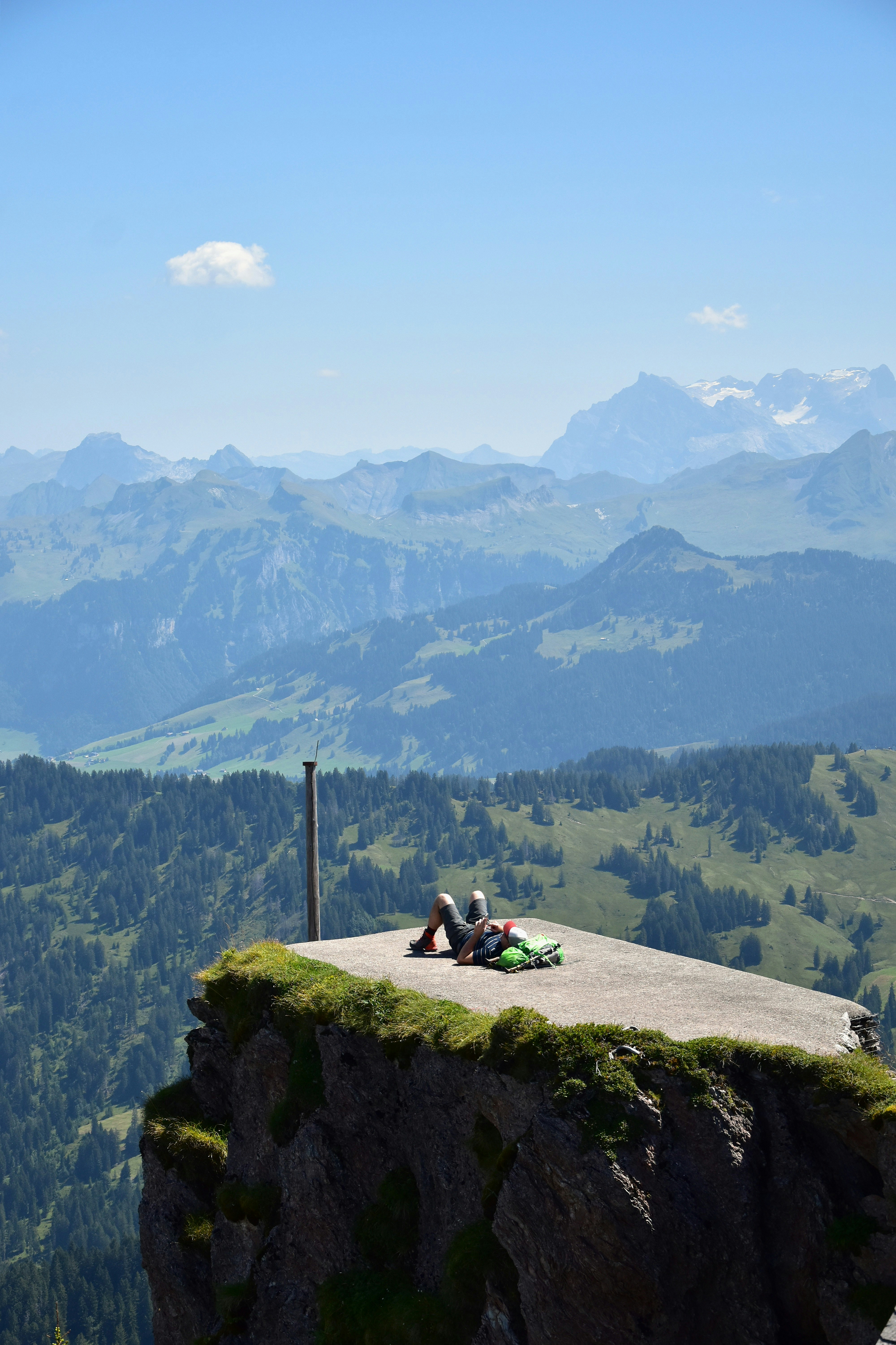 Summit Rest: Hiker on a Cliff Edge with Layered Alpine Vistas
