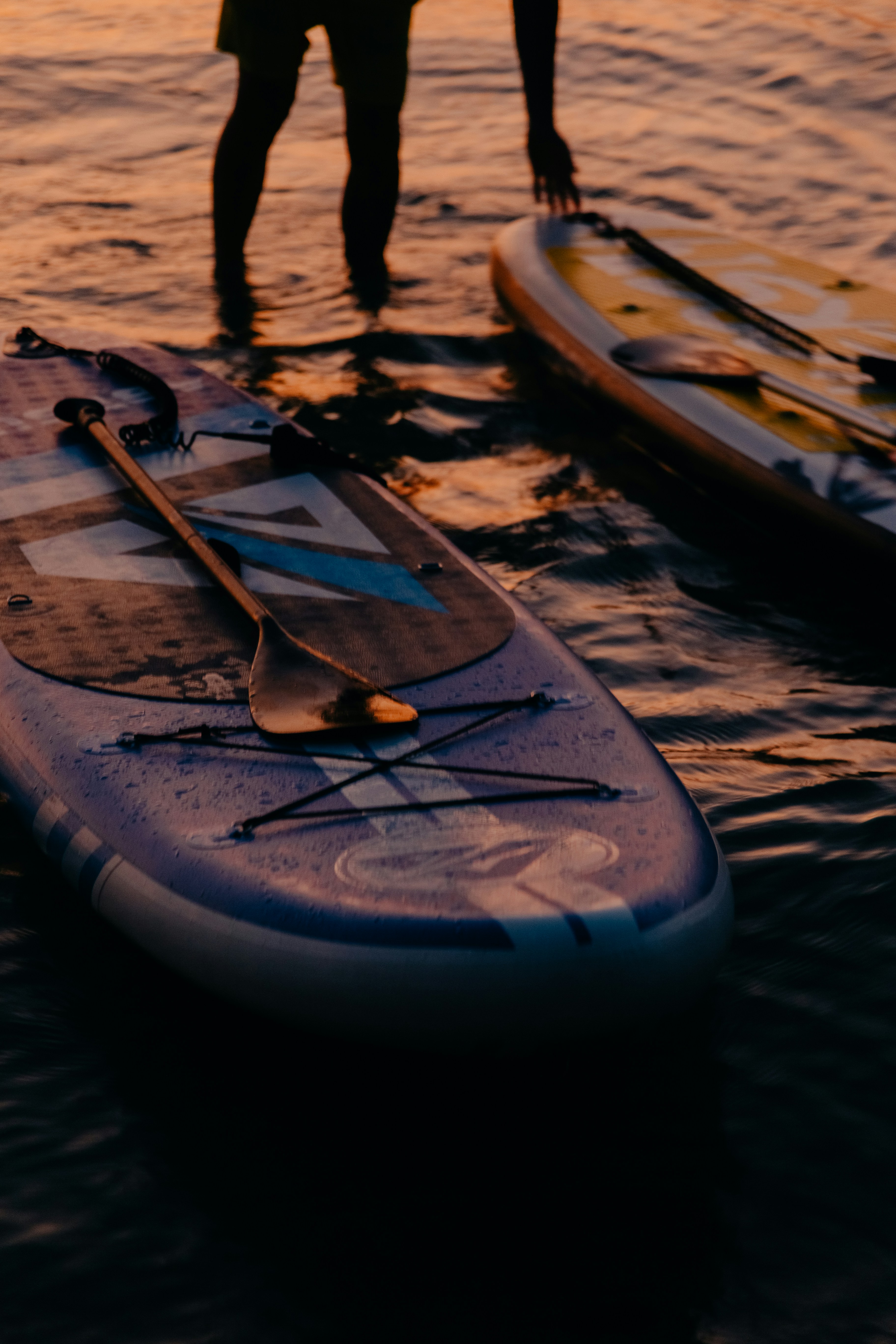 Two Stand-Up Boards Rest at Sunset, Water Lit by Warm Glow