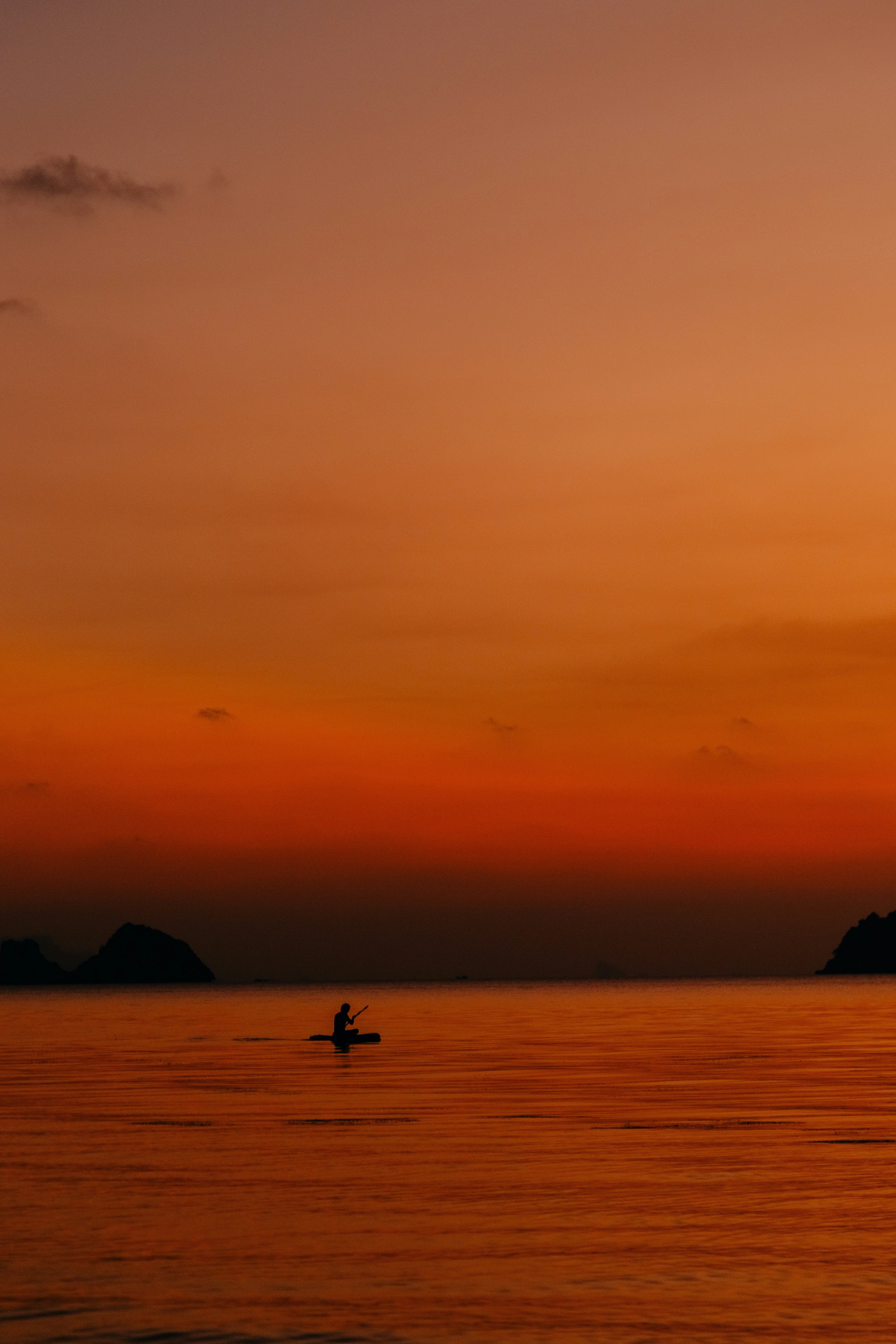 Silhouette in a Fiery Sea: A Lone Rowing Figure at Dusk