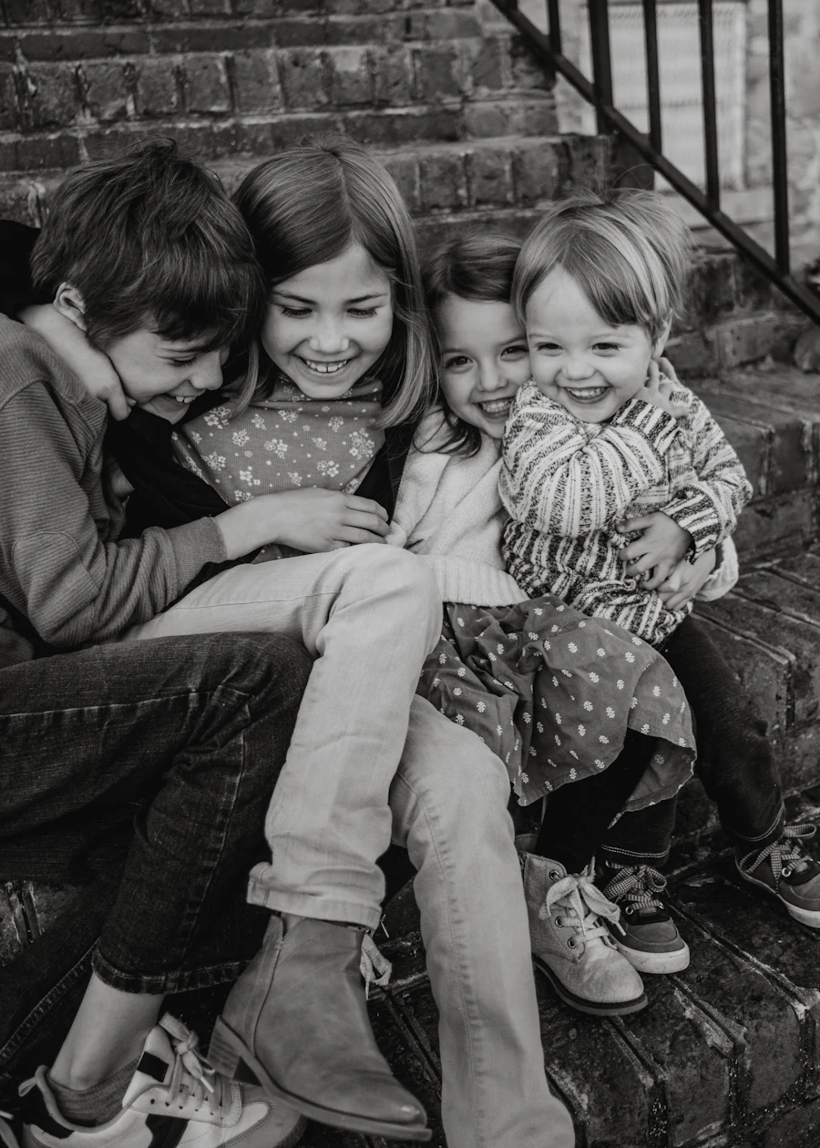 Group of four children sit on brick steps, sharing a warm moment with smiles and closeness; black-and-white portrait emphasizing affection and texture.