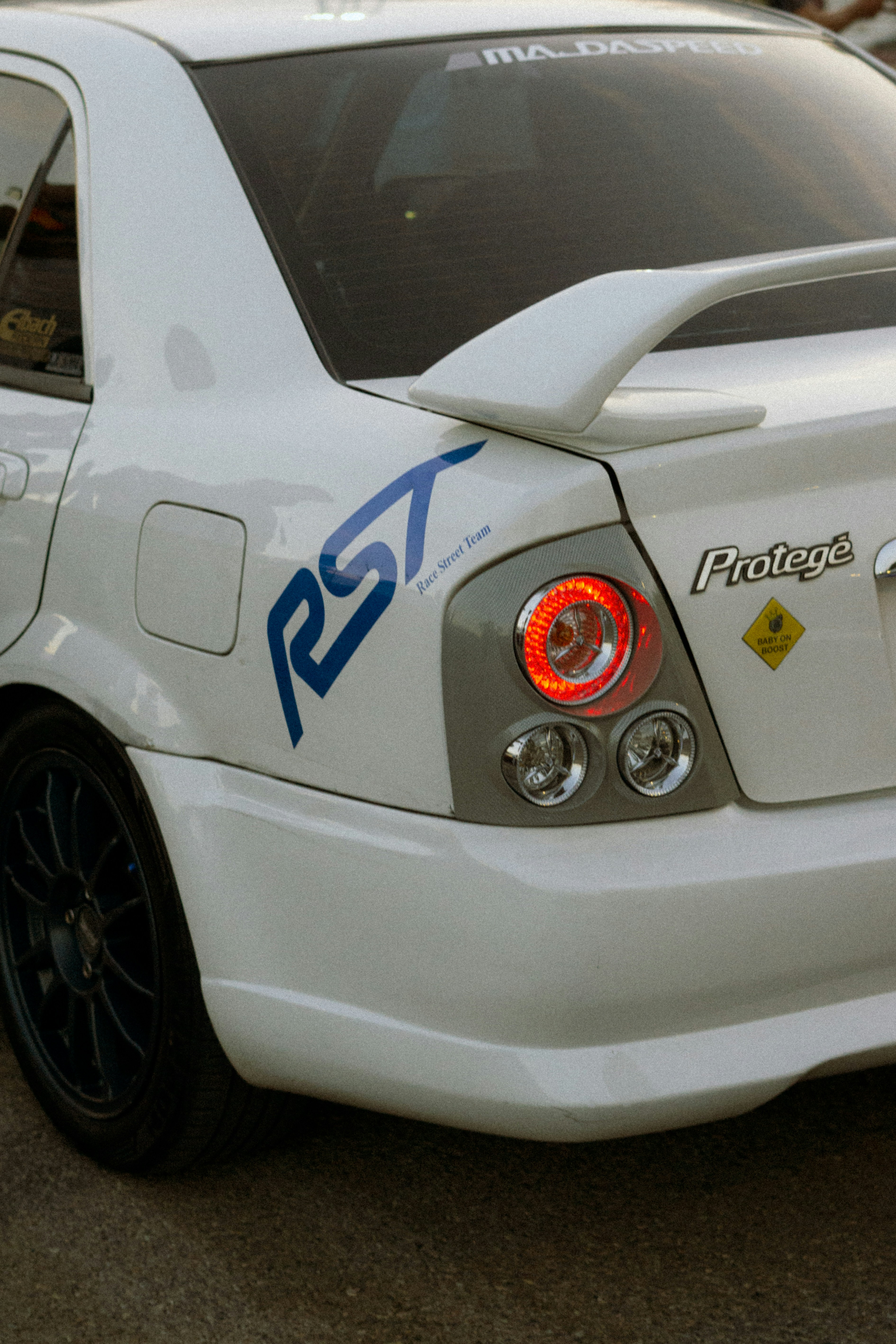 White hatchback sprinting toward the camera: rear quarter panel with blue RS7 decal and red tail light
